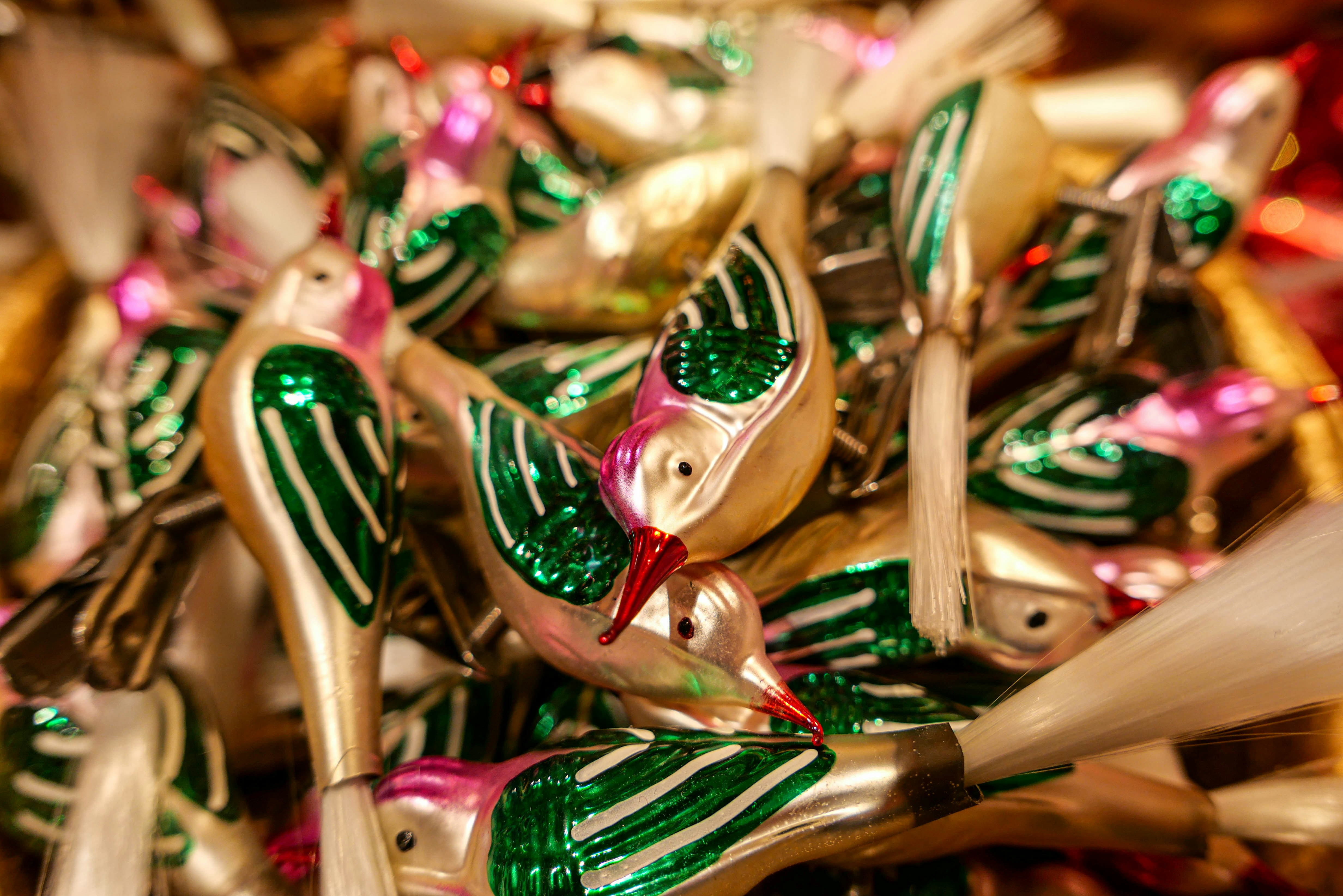 Colorful decorative bird ornaments with shiny finishes nestled together in a woven basket.