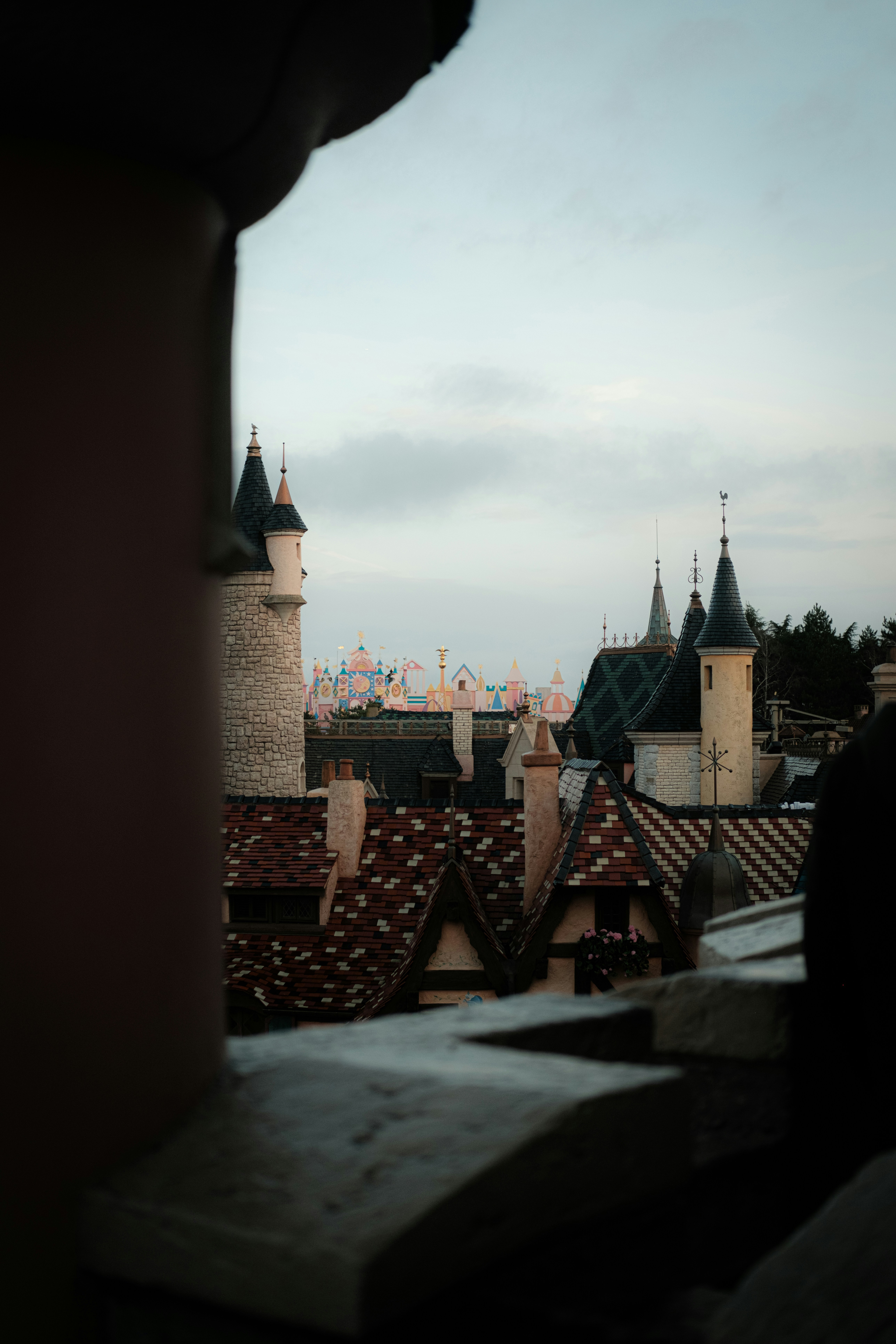 Distant pastel castle towers on the horizon, framed by dark, silhouetted foreground rooftops.