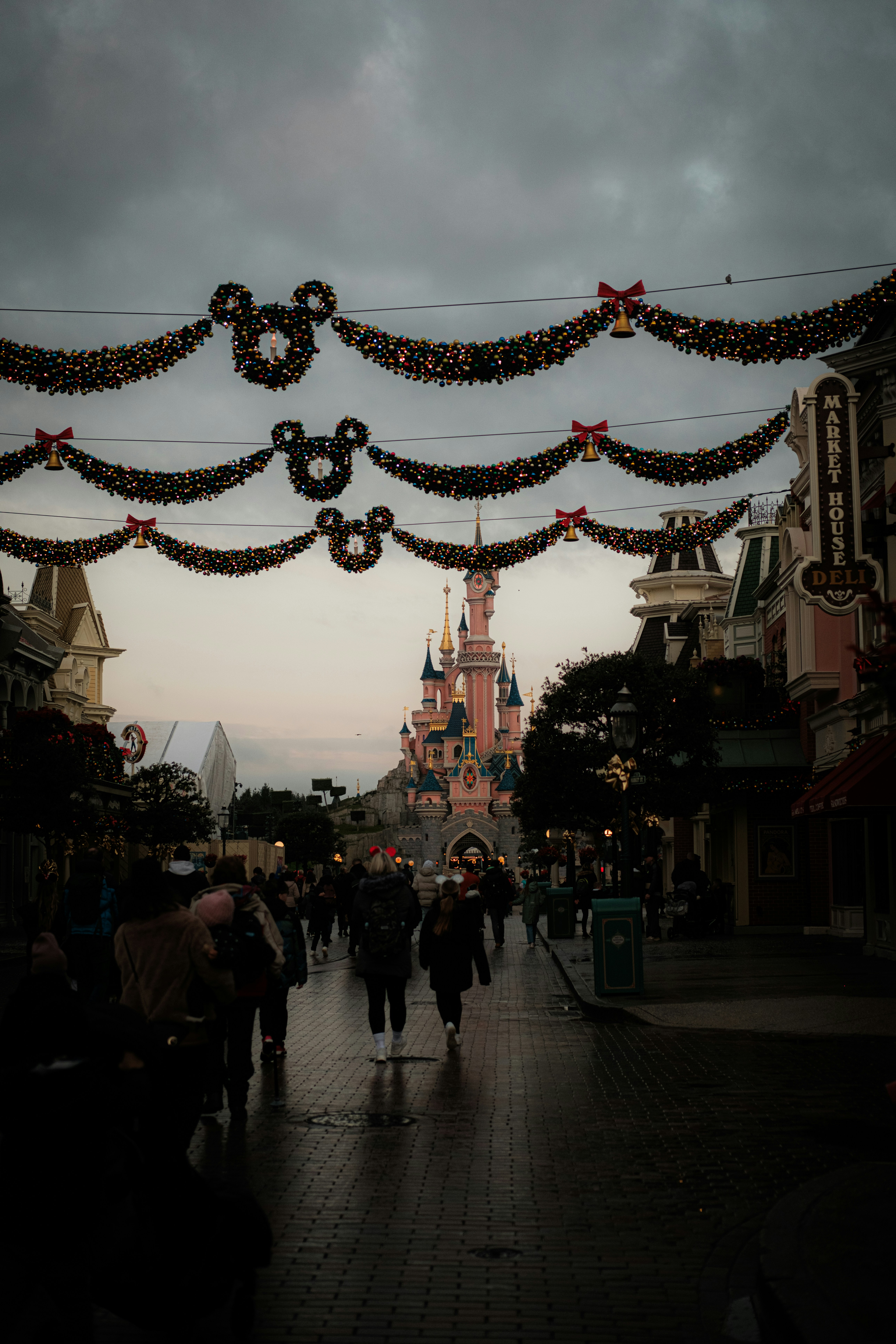 Festive decorations arch over a bustling street leading to a whimsical castle at dusk, capturing the magic of the moment.
