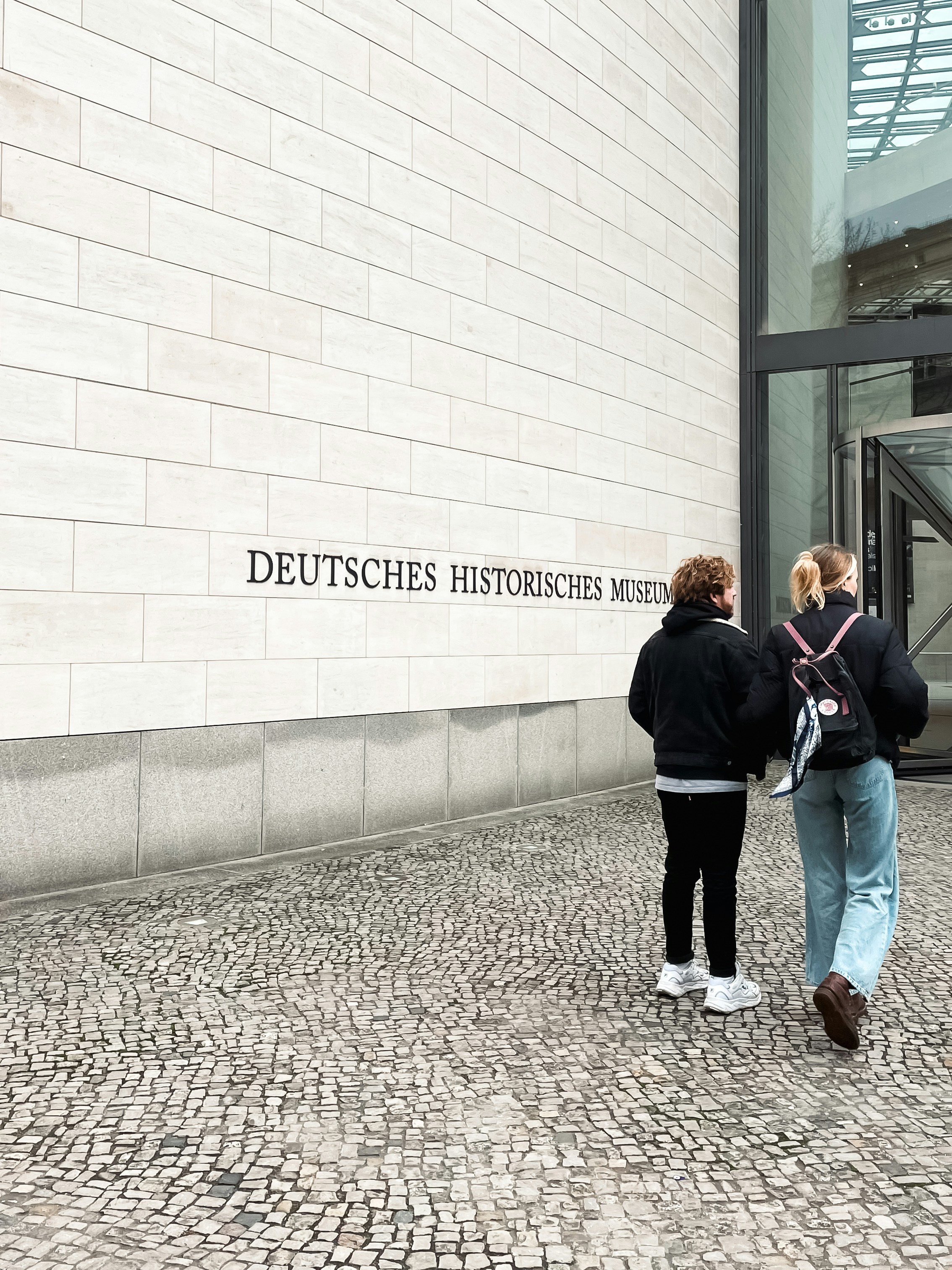 Visitors walking towards the entrance of the Deutsches Historisches Museum, framed by modern architecture and cobblestone pathways.