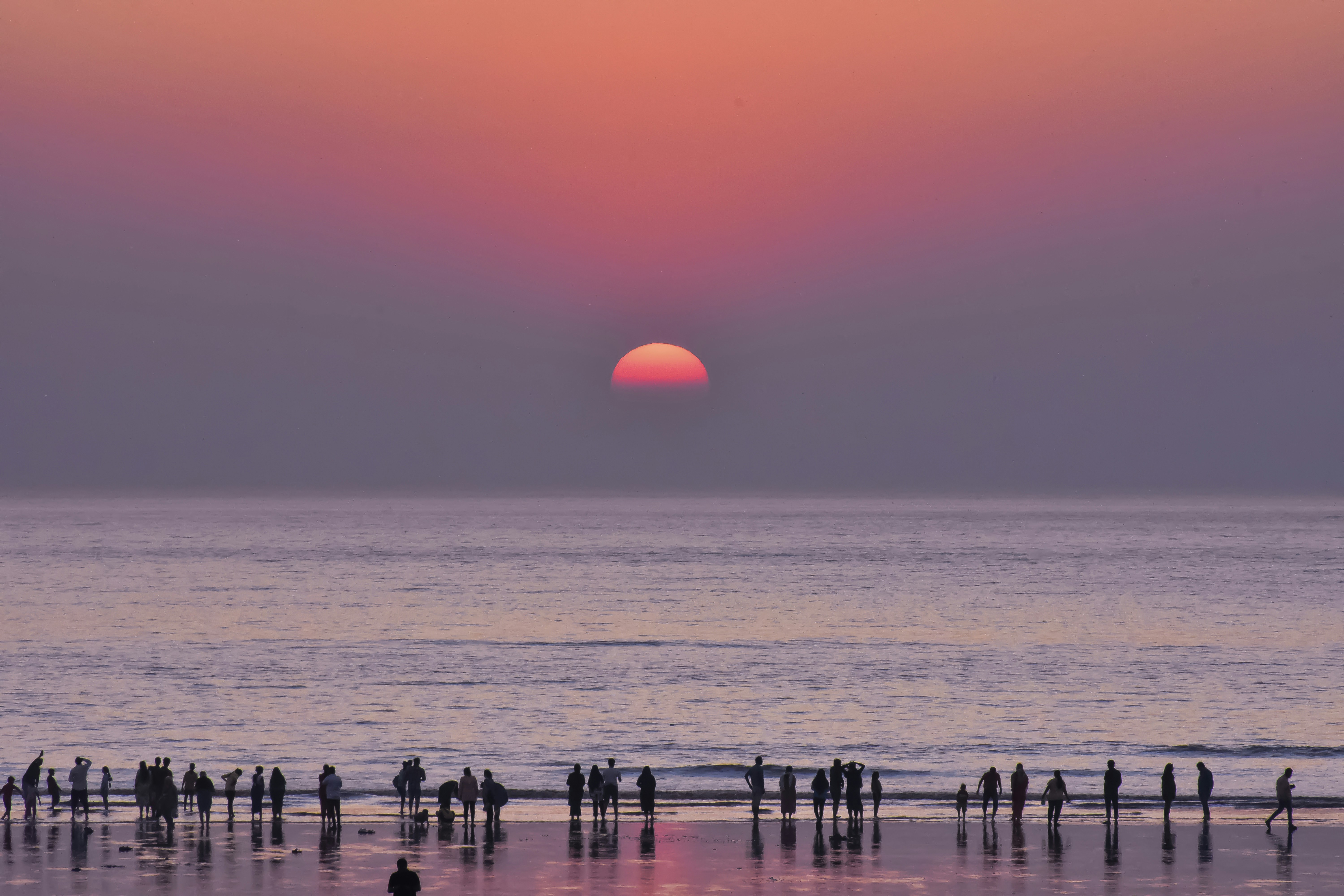 Sunset over Dandi Beach with silhouetted figures wading in the tranquil sea.