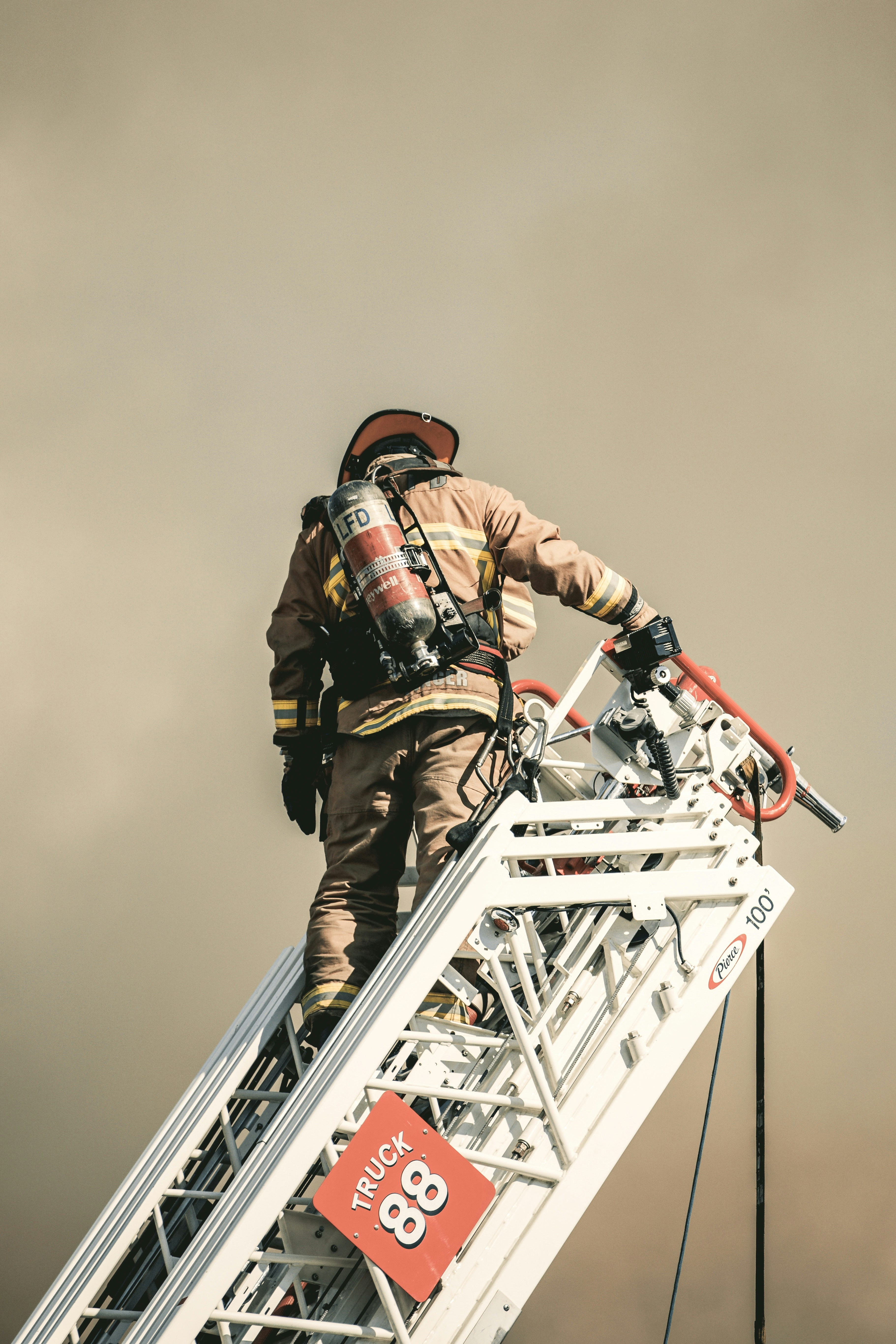 Firefighter climbing a ladder towards a smoky sky, equipped with essential gear and a fire hose. The scene captures the essence of bravery and determination.