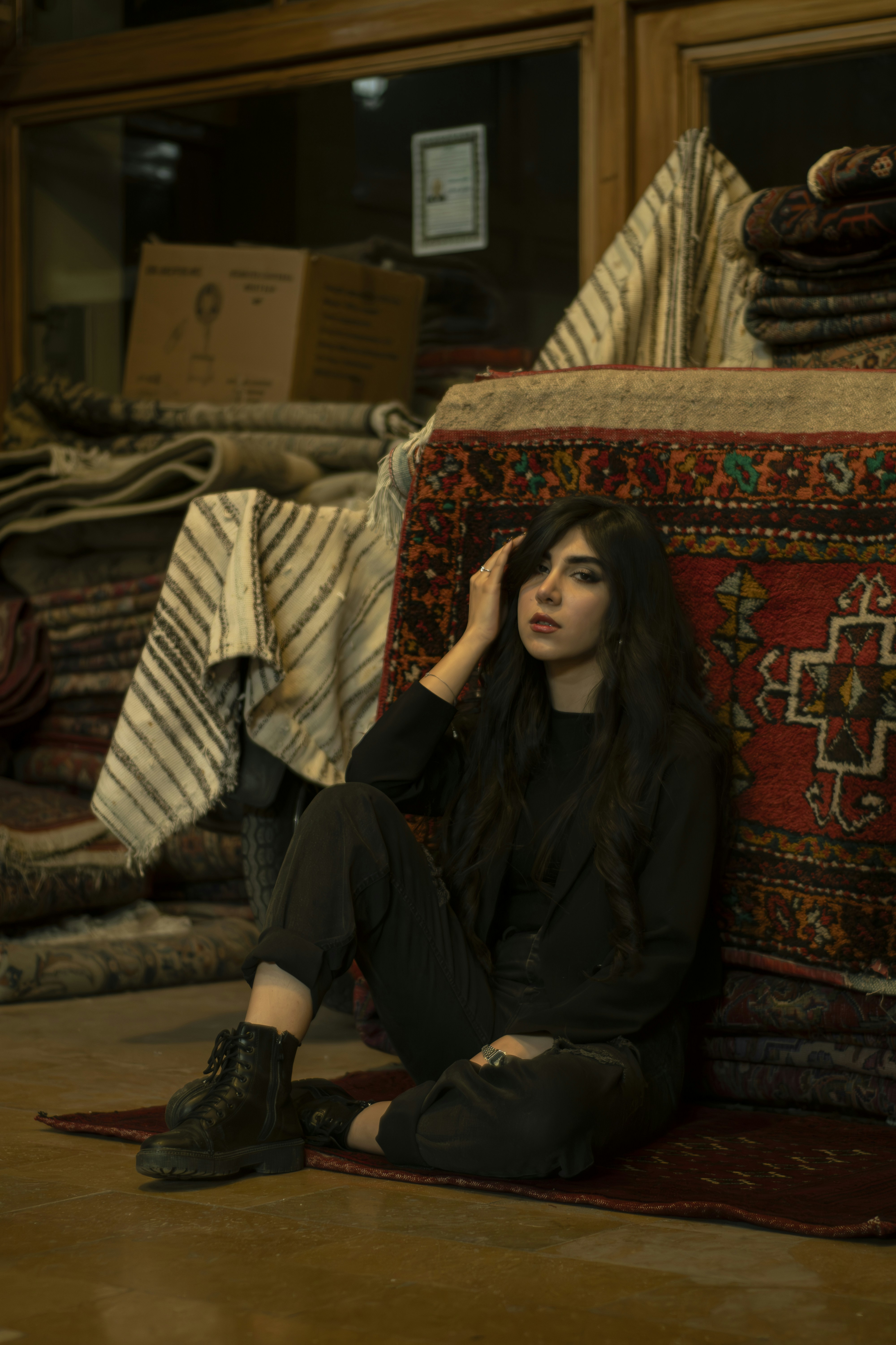 A woman sitting on the floor next to a pile of rugs photo – Free Tehran ...