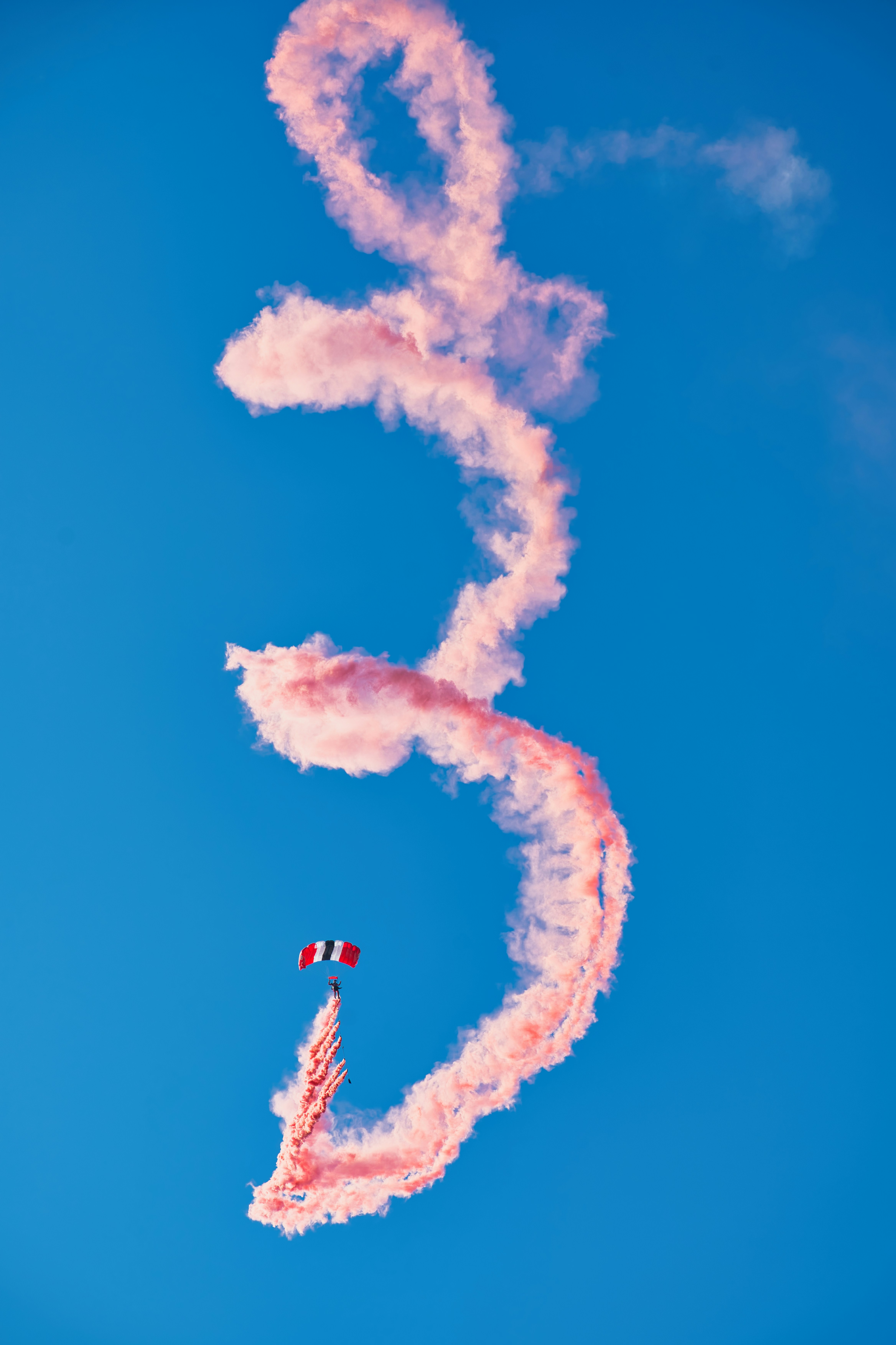 Crimson Spiral: A Parachutist's Smoke Serpent Rises Through Azure