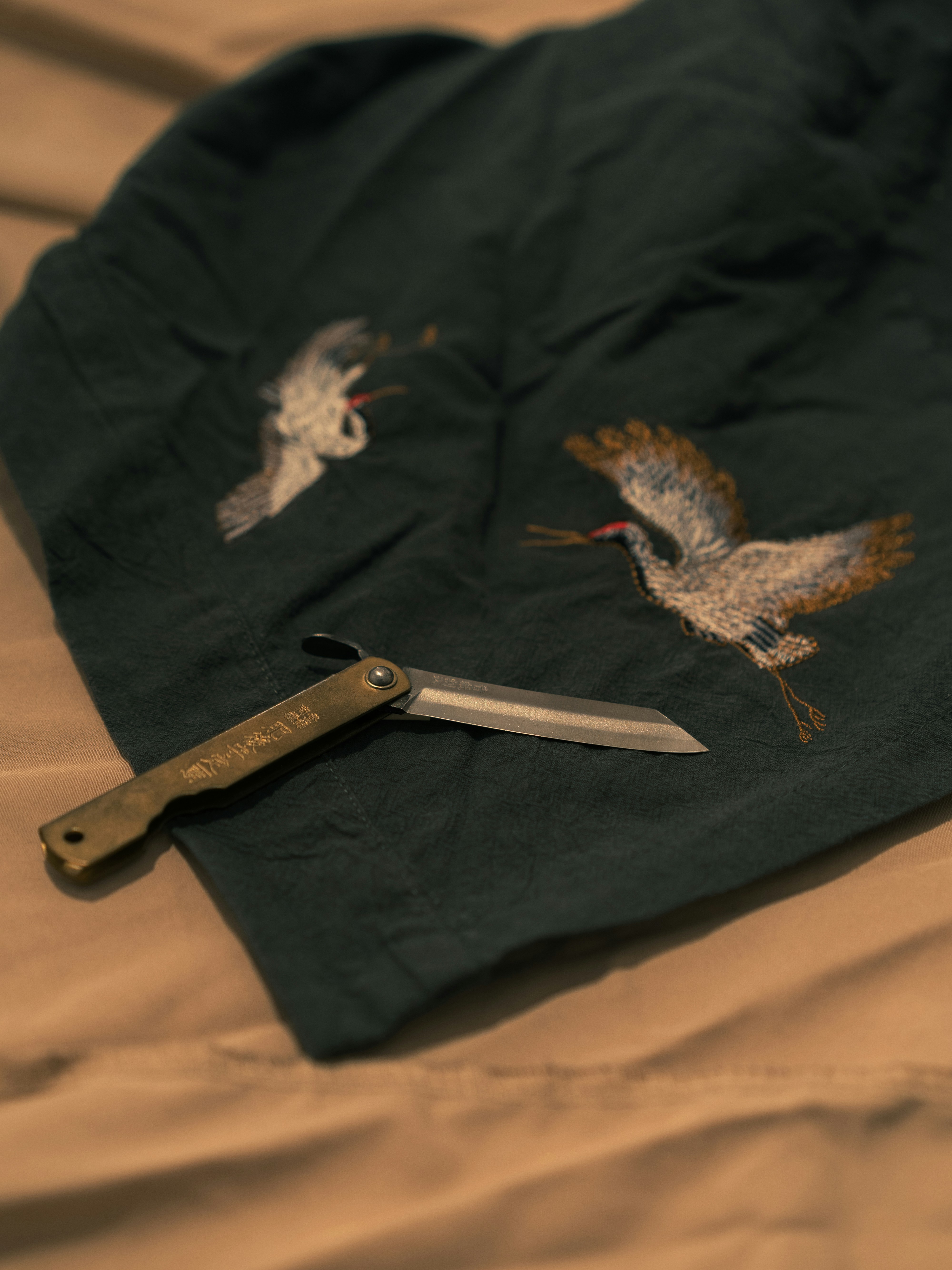 Slip of Steel on Silk: Folding Knife Resting Among Crane Embroidery