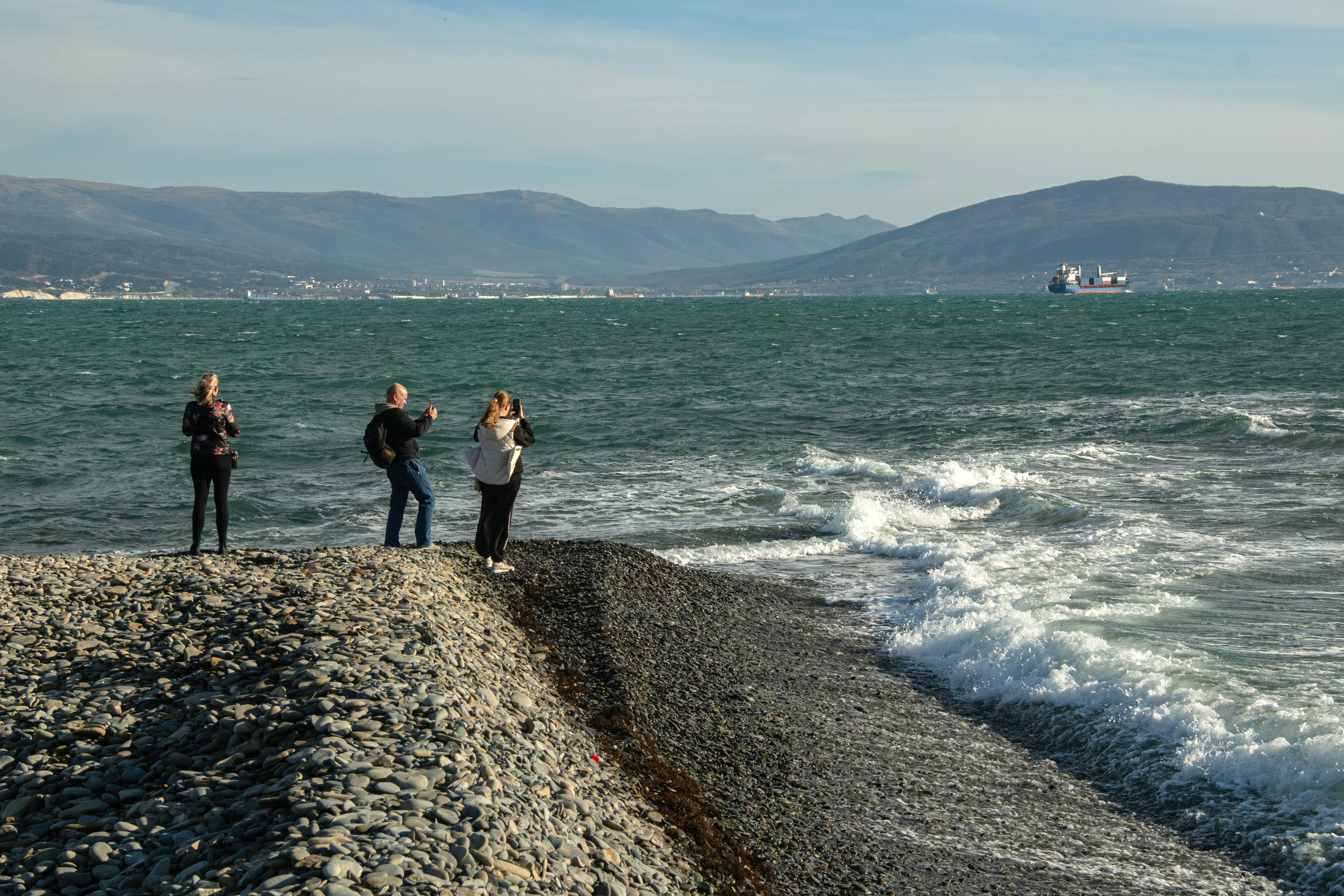 Three on the Pebble Breakwater: A Quiet Moment Facing the Open Sea