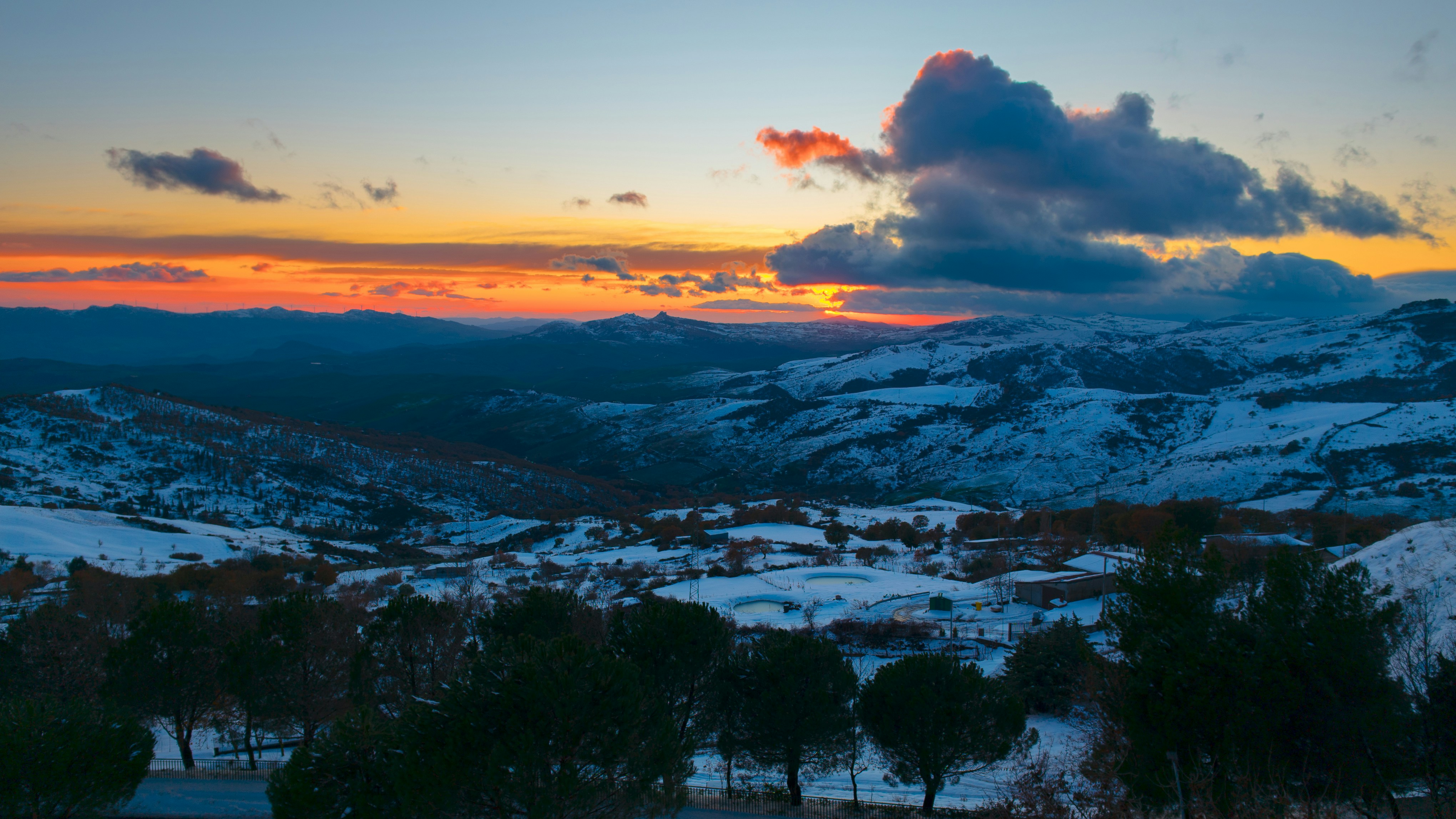 The sun is setting over a snowy mountain range