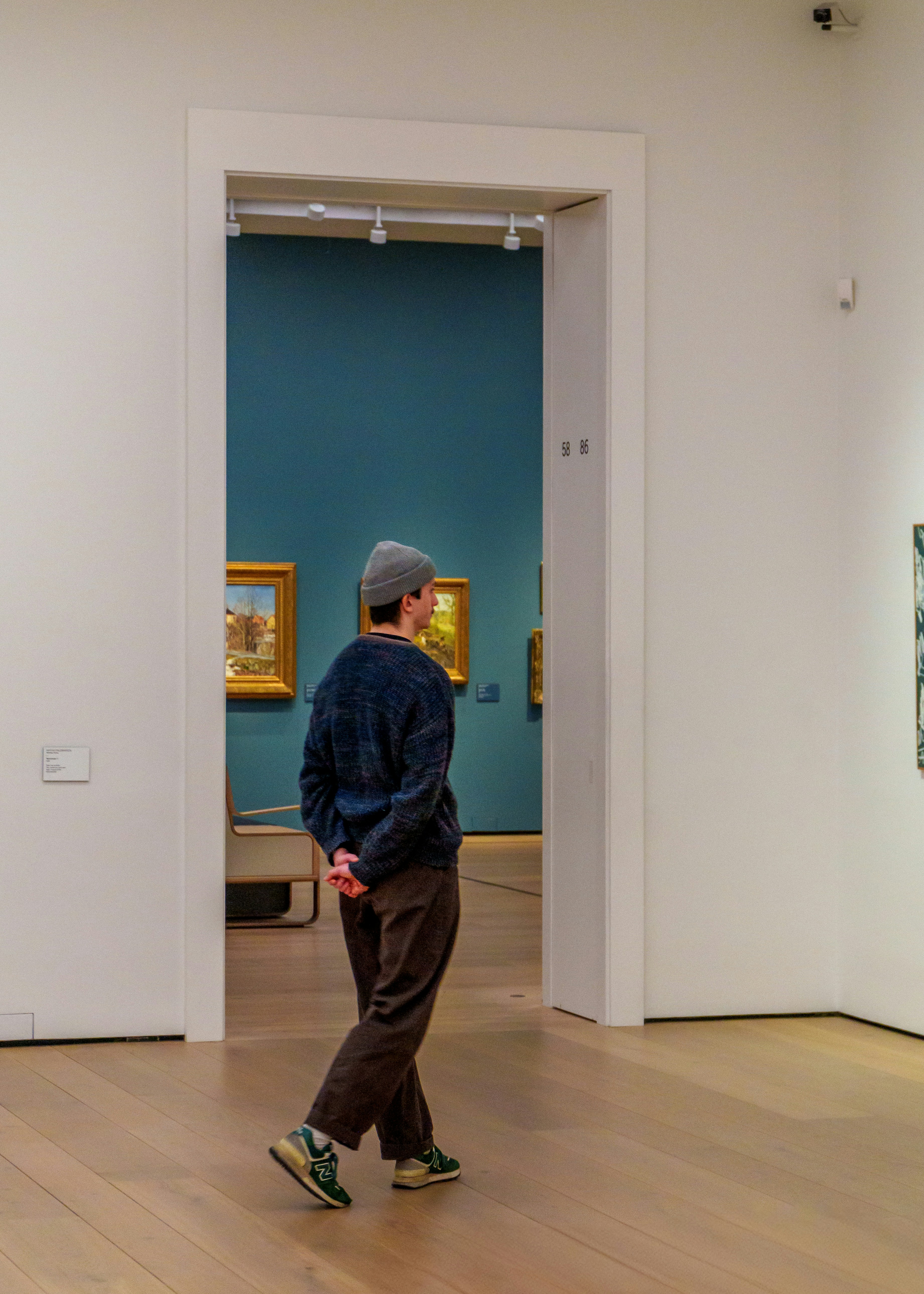 Visitor walking through an art gallery doorway, framed by walls adorned with paintings and a striking blue backdrop.