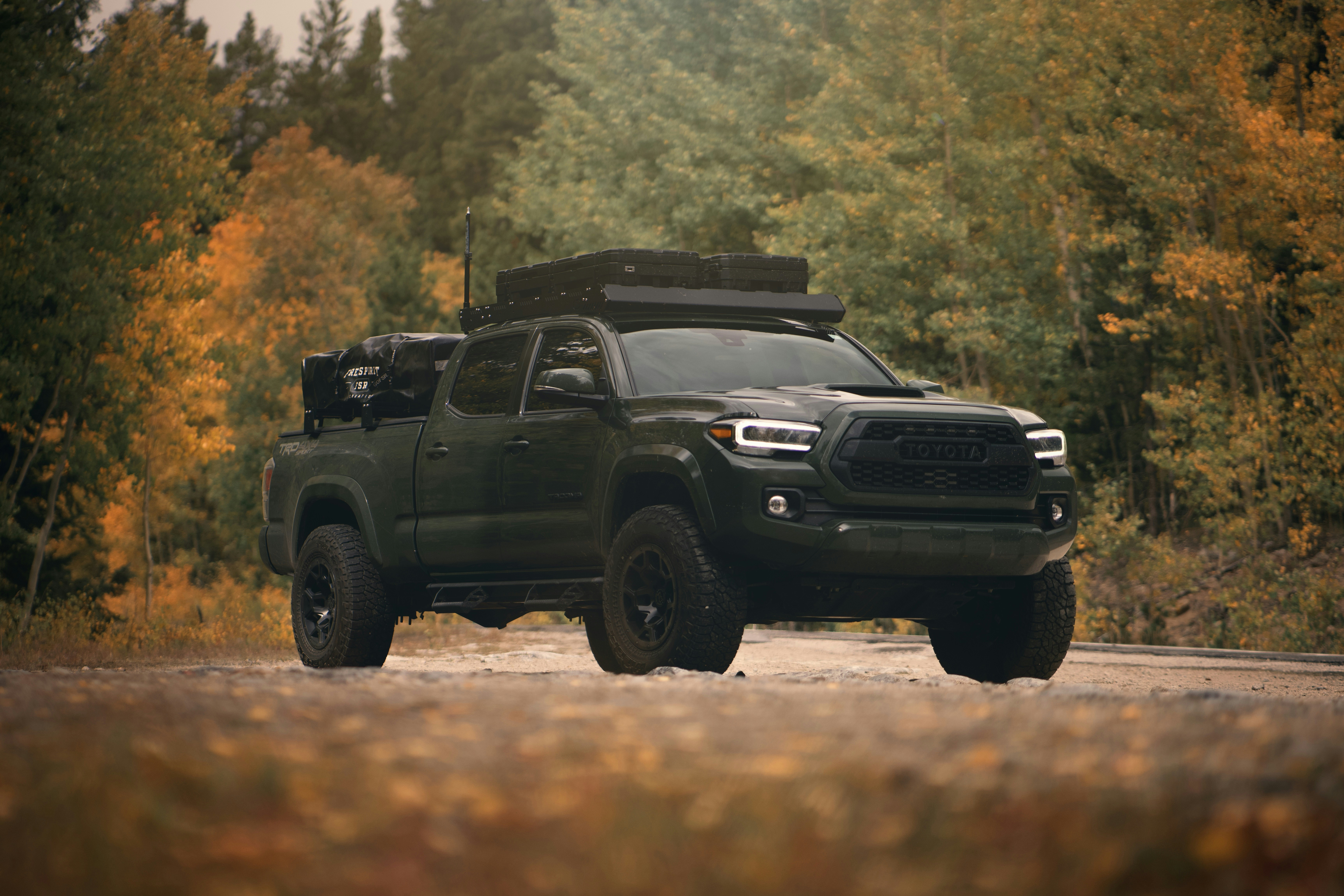 Dark green off-road truck parked on a forest path surrounded by vibrant autumn leaves.
