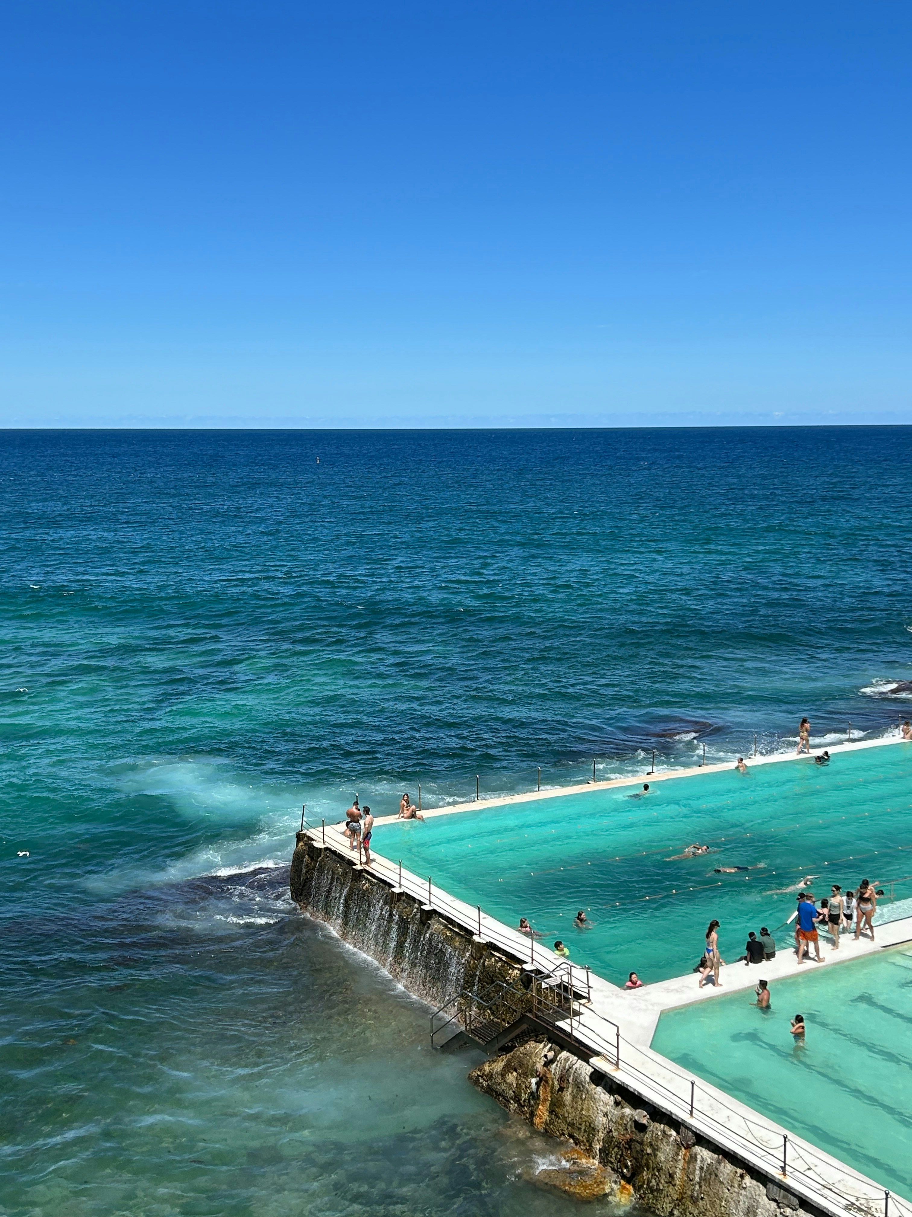 Turquoise Terrace by the Sea: A cliffside pool teeming with sunlit swimmers