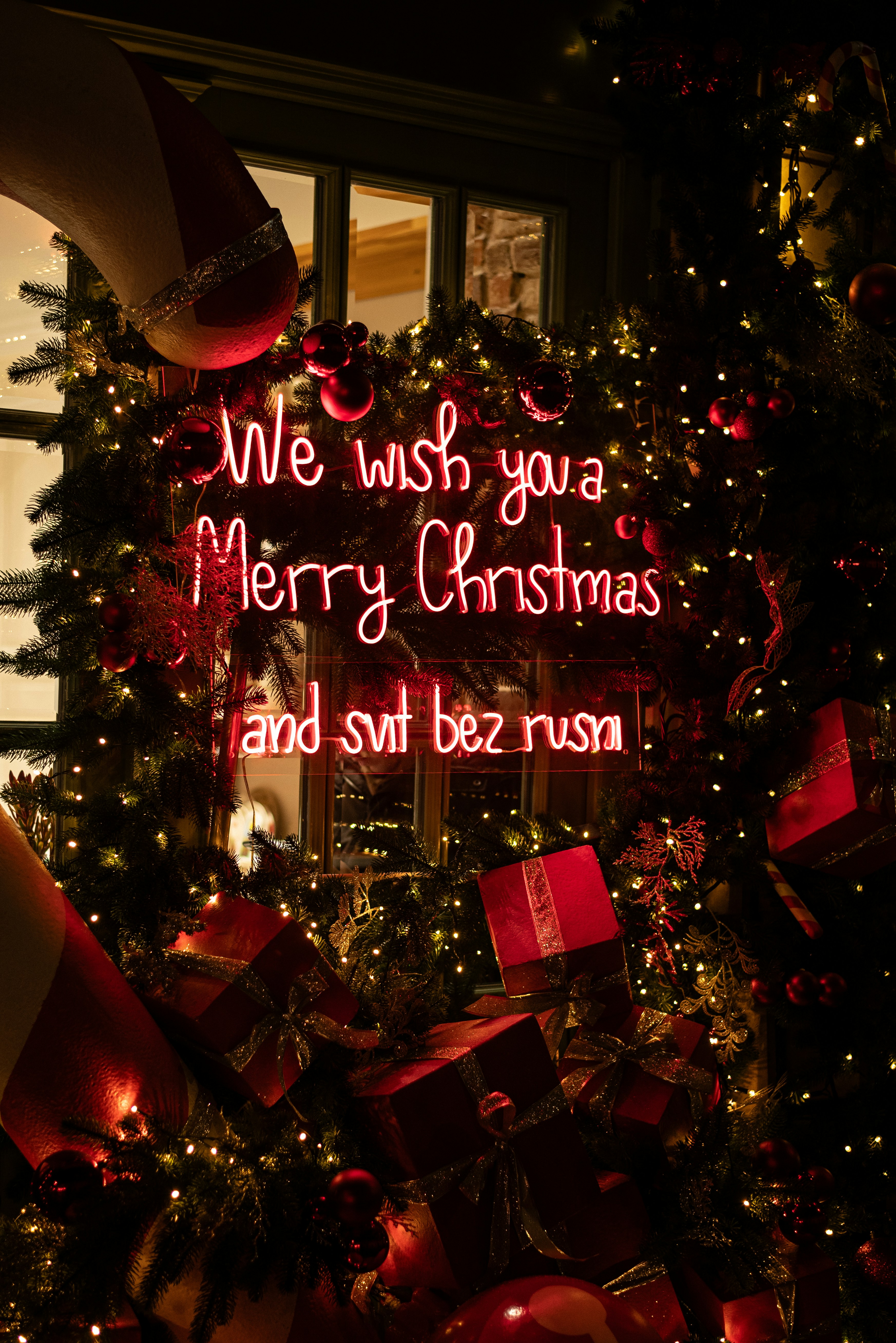 Neon sign wishing a Merry Christmas surrounded by festive decorations and gifts. Warm lights enhance the holiday spirit.