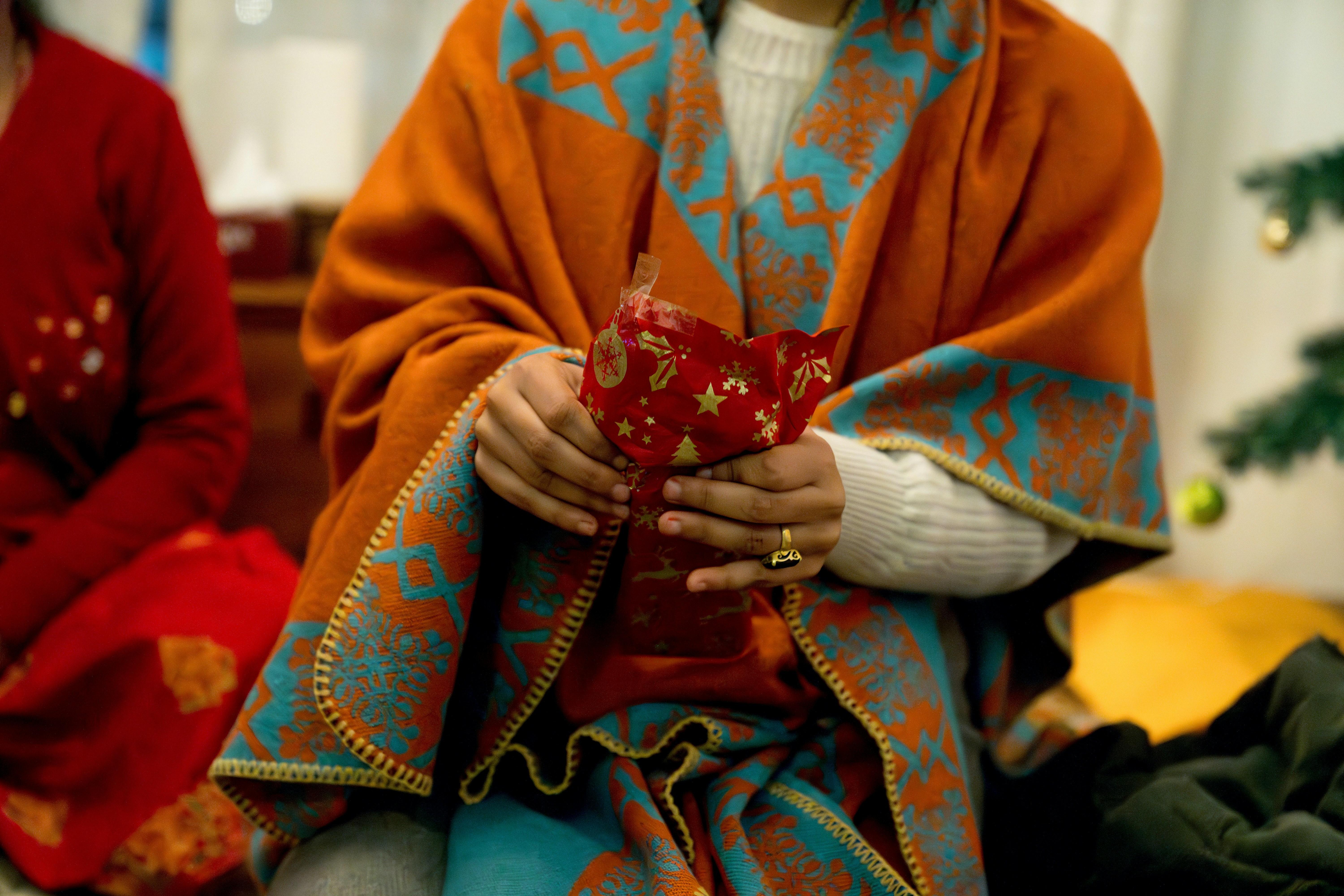 Hands Cradle a Festive Red Pouch Inside a Turquoise-Trimmed Cloak
