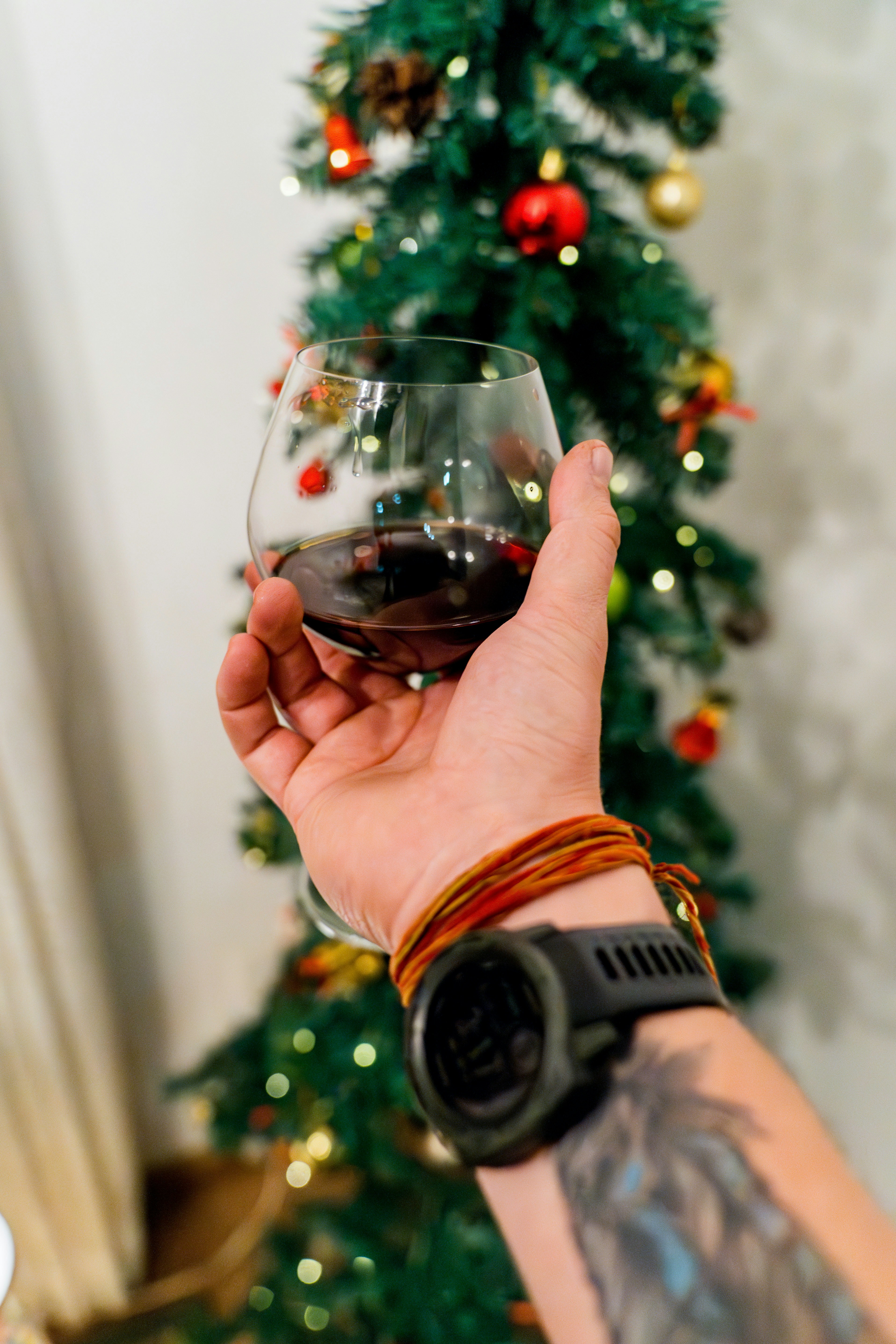 A Toast Beside the Glow: Hand, Wine Glass, and Holiday Tree