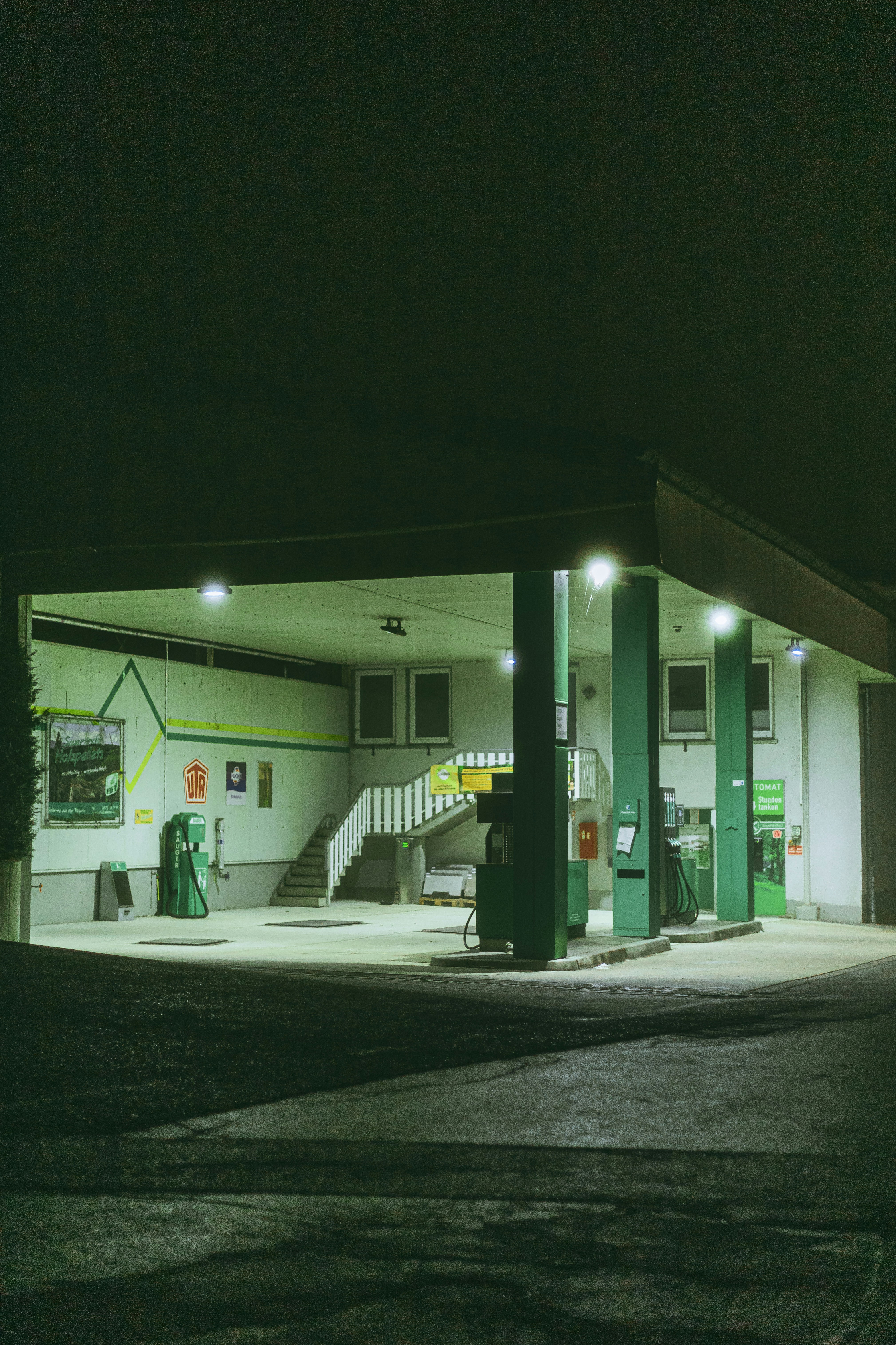 Gas station at night, featuring bright lights illuminating the pumps and stairs. The quiet scene evokes a sense of stillness.