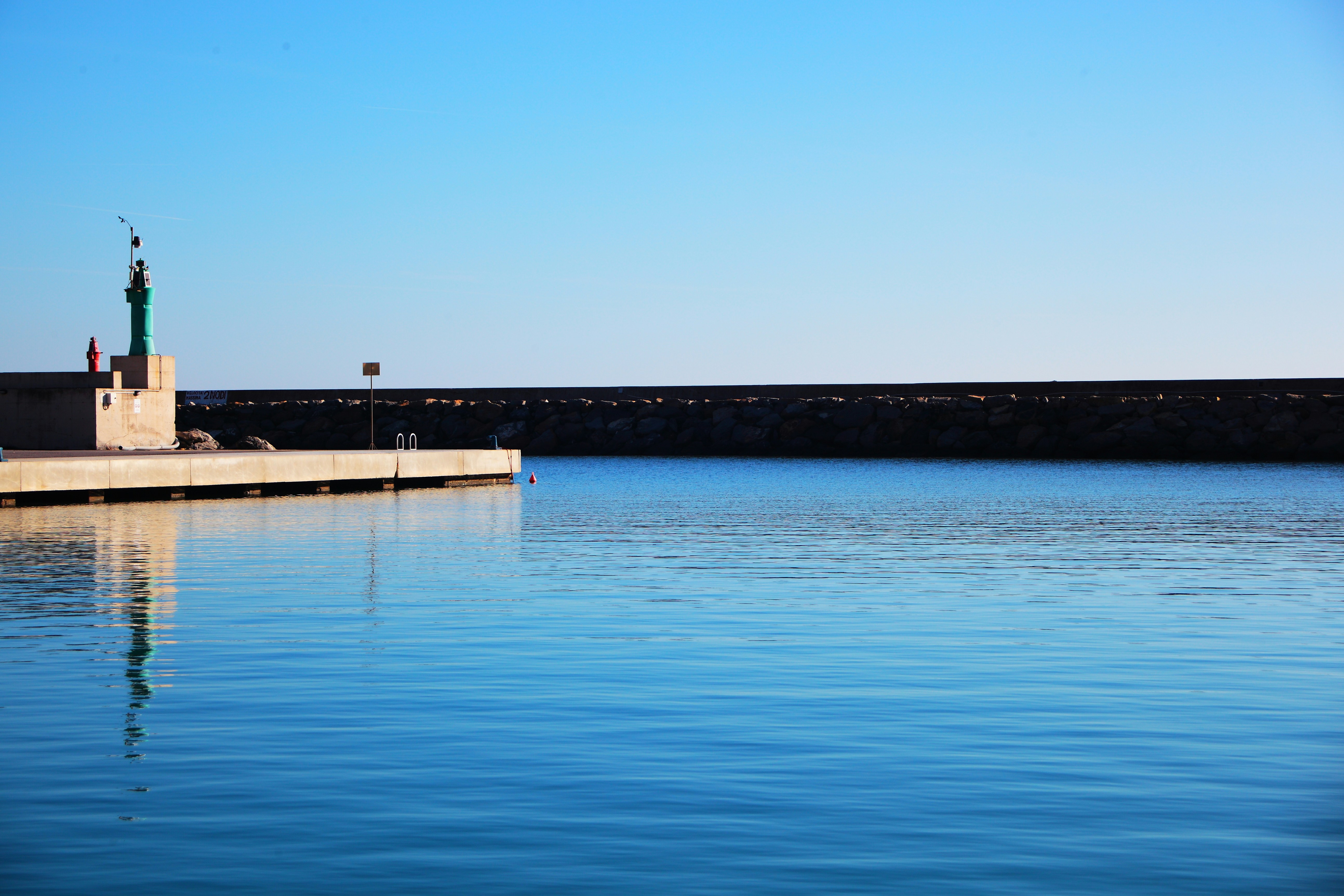 Lighthouse standing on a calm blue waterfront under a clear sky.