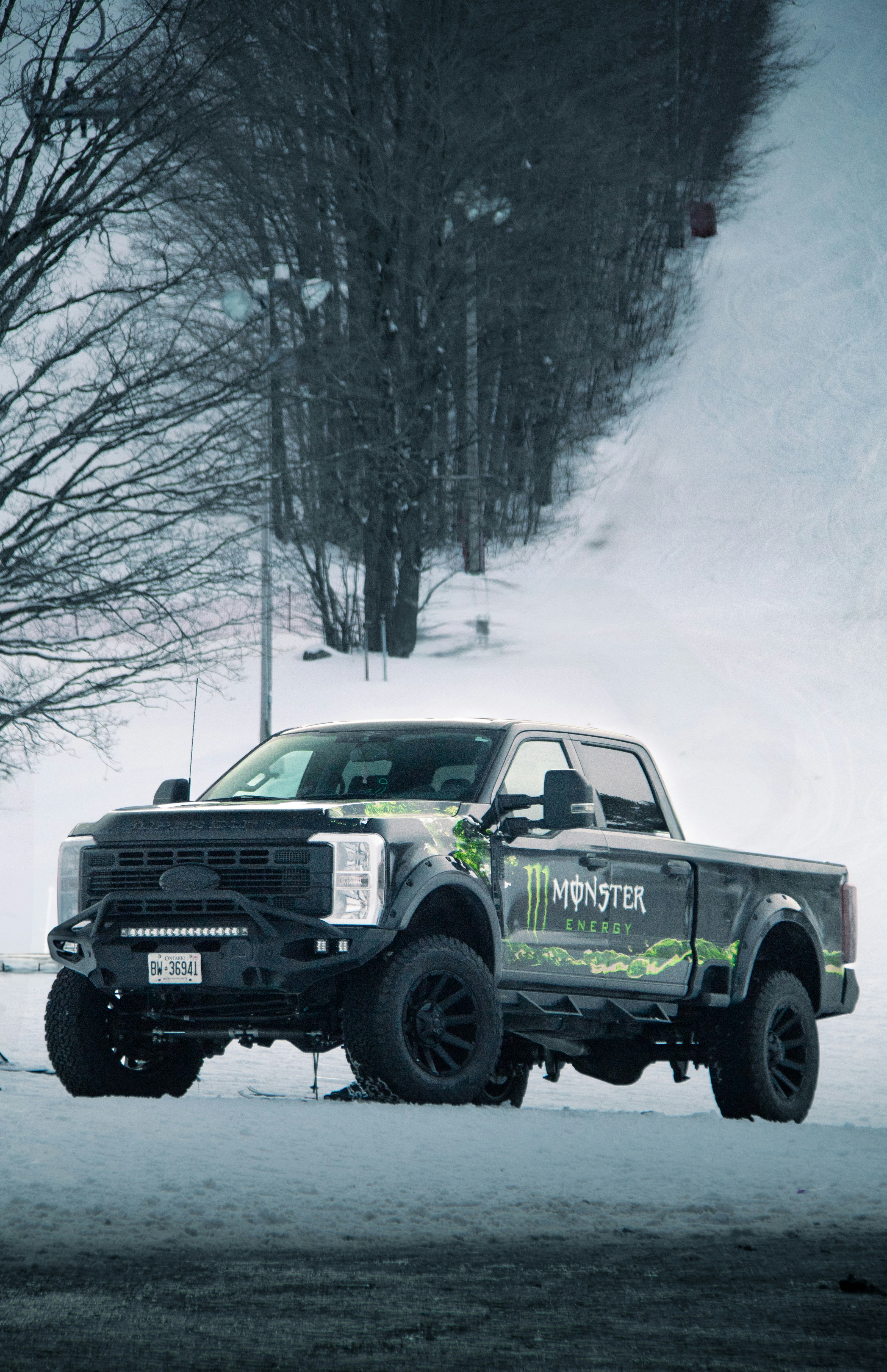 Black truck with green decals parked on snow-covered landscape near leafless trees.