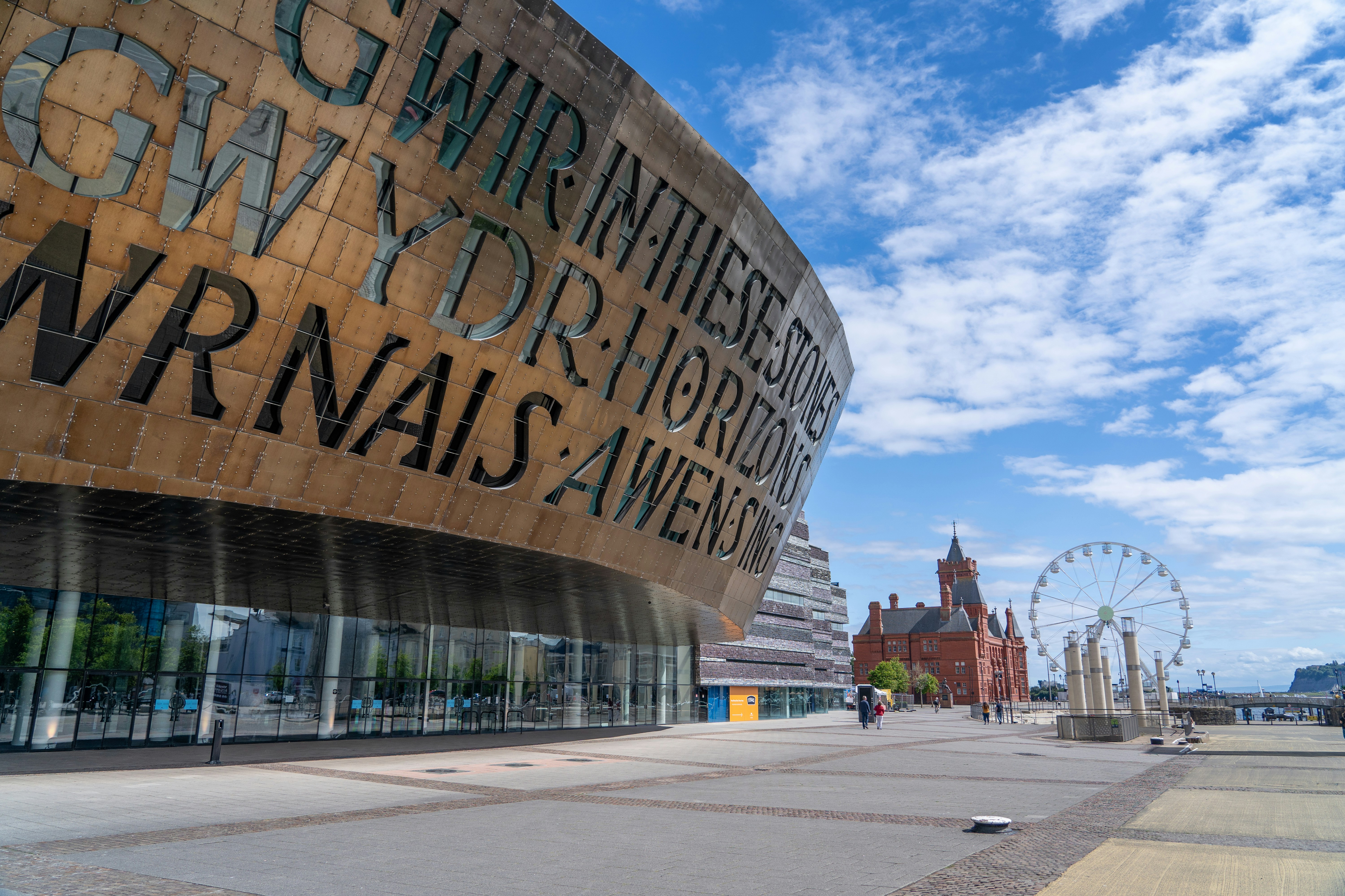 Modern copper-clad building with inscribed letters beside a Ferris wheel under a vibrant blue sky.