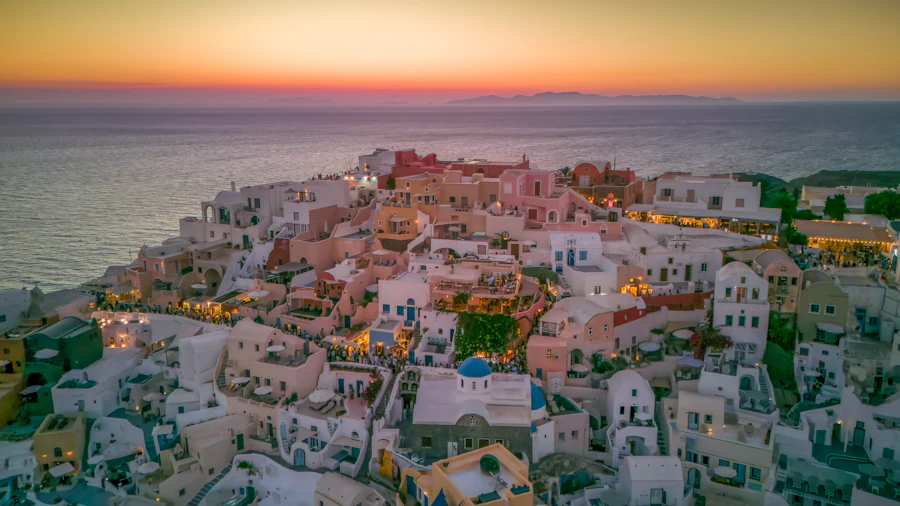 White-washed cliffside village with clustered houses and a single blue-domed church lit at sunset over the Aegean Sea.