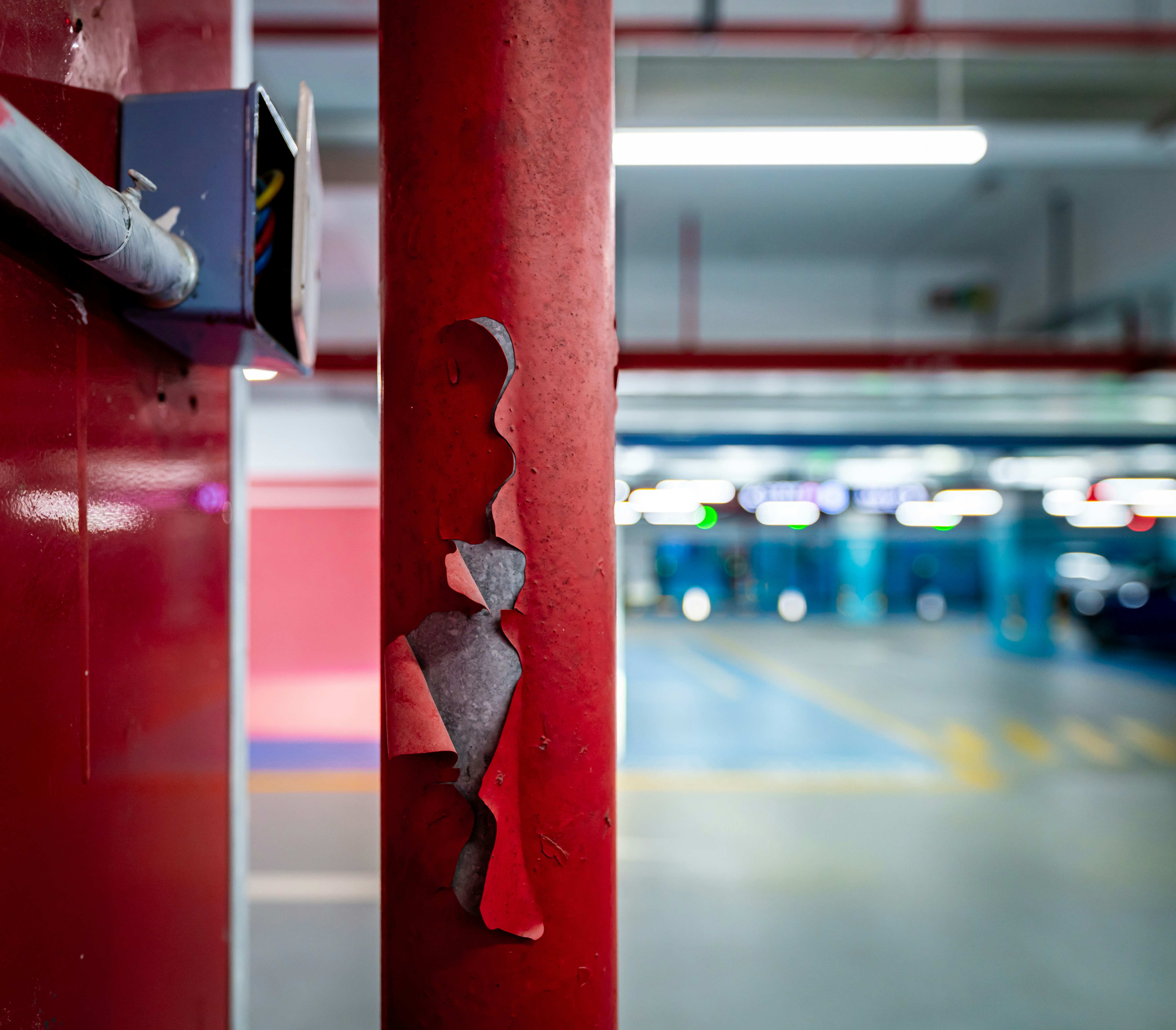 Crimson Pillar Portrait: Peeling Paint Amid Neon Blur in a Parking Garage