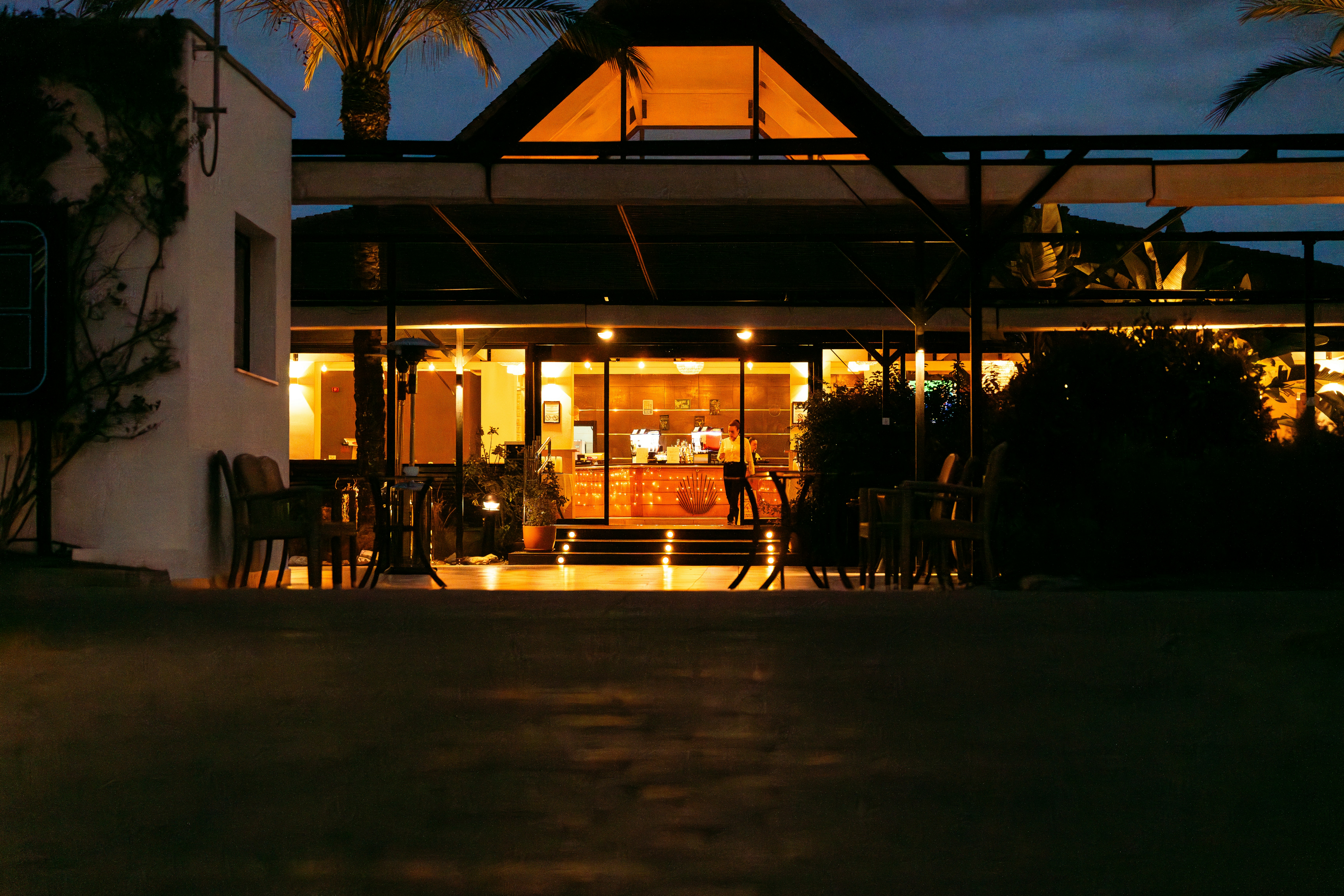 Warmly lit poolside bar under a twilight sky with palm trees silhouetted in the background.