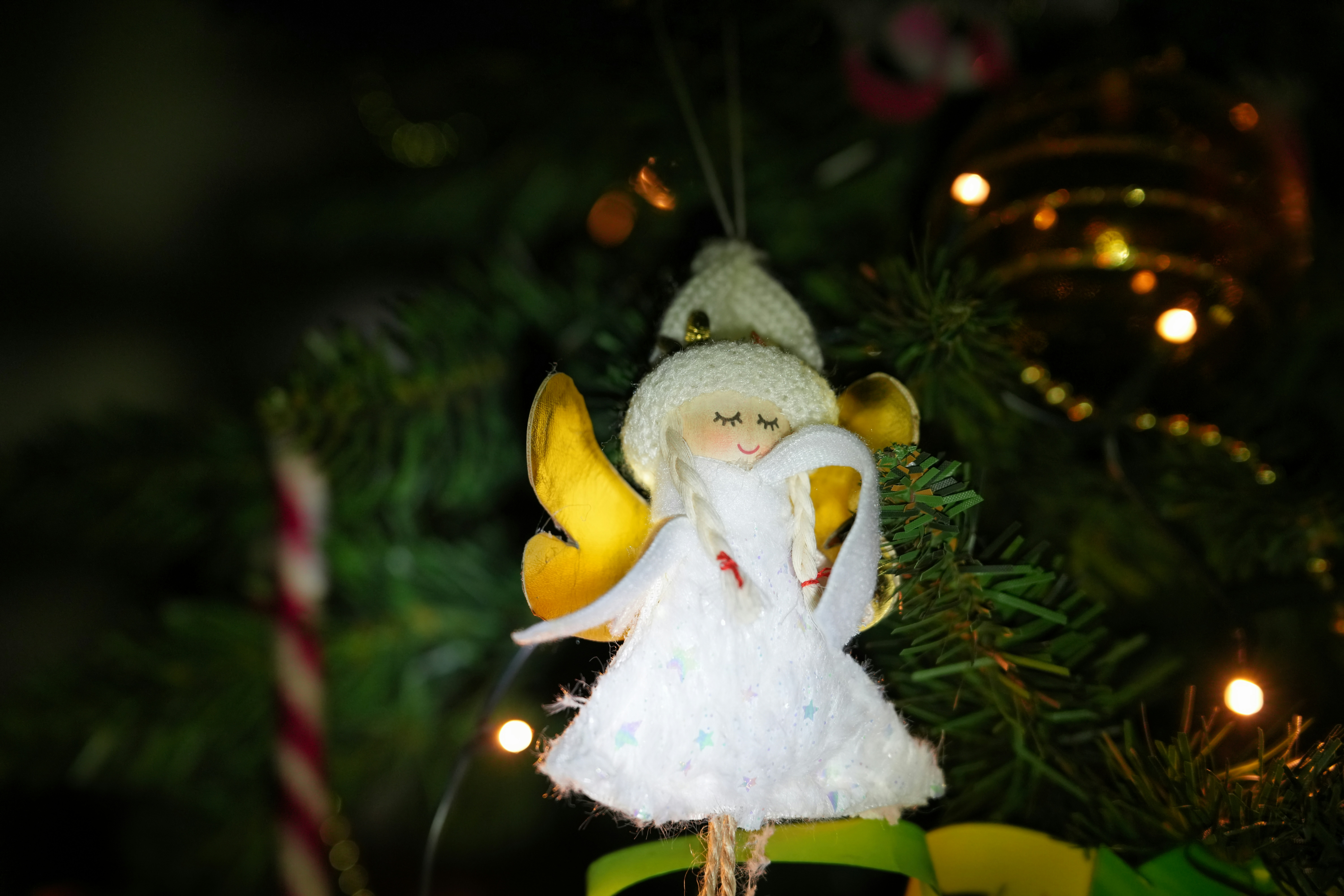 Handmade angel ornament with golden wings nestled among vibrant tree branches and festive lights.