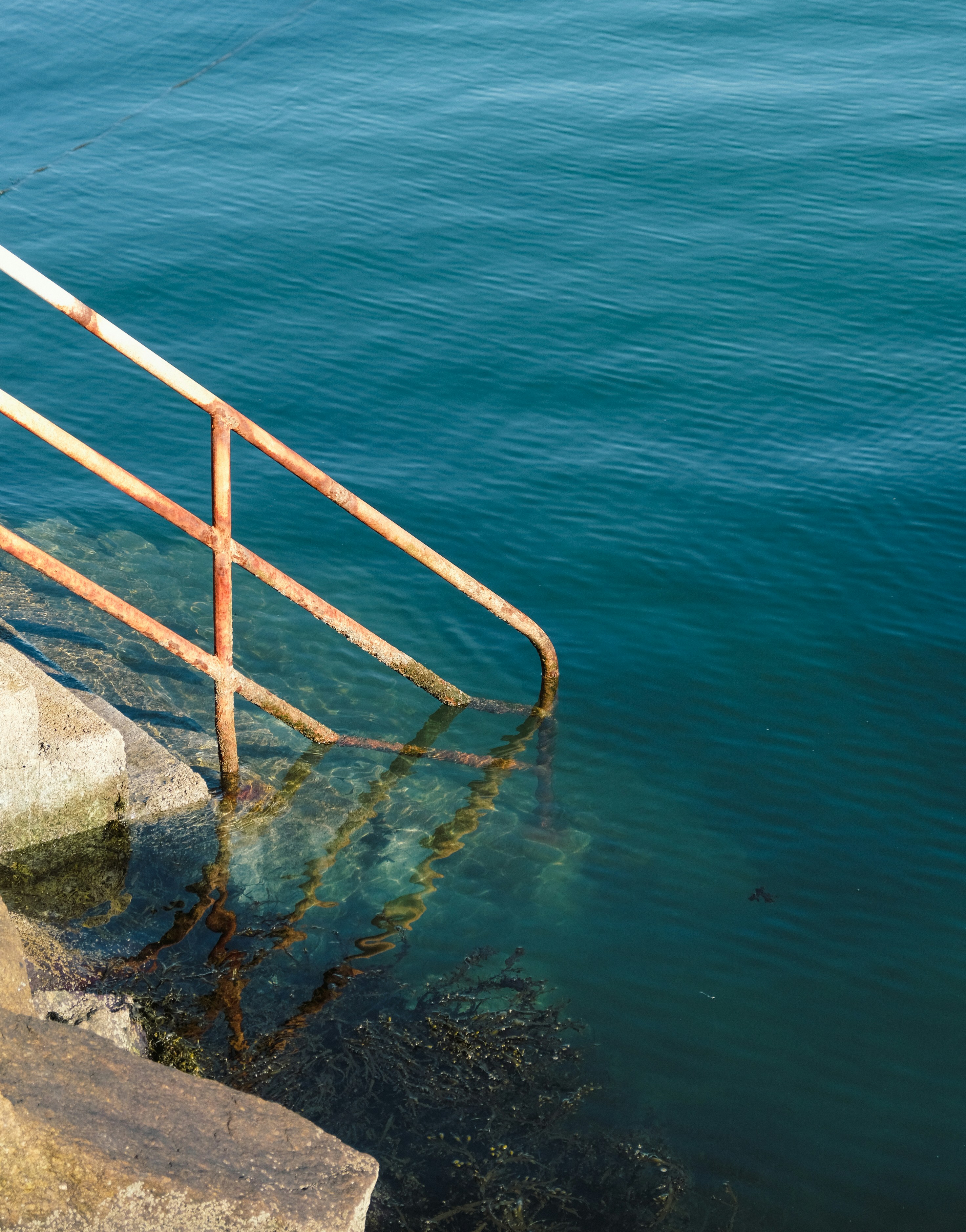 Rusty railing descends into turquoise calm