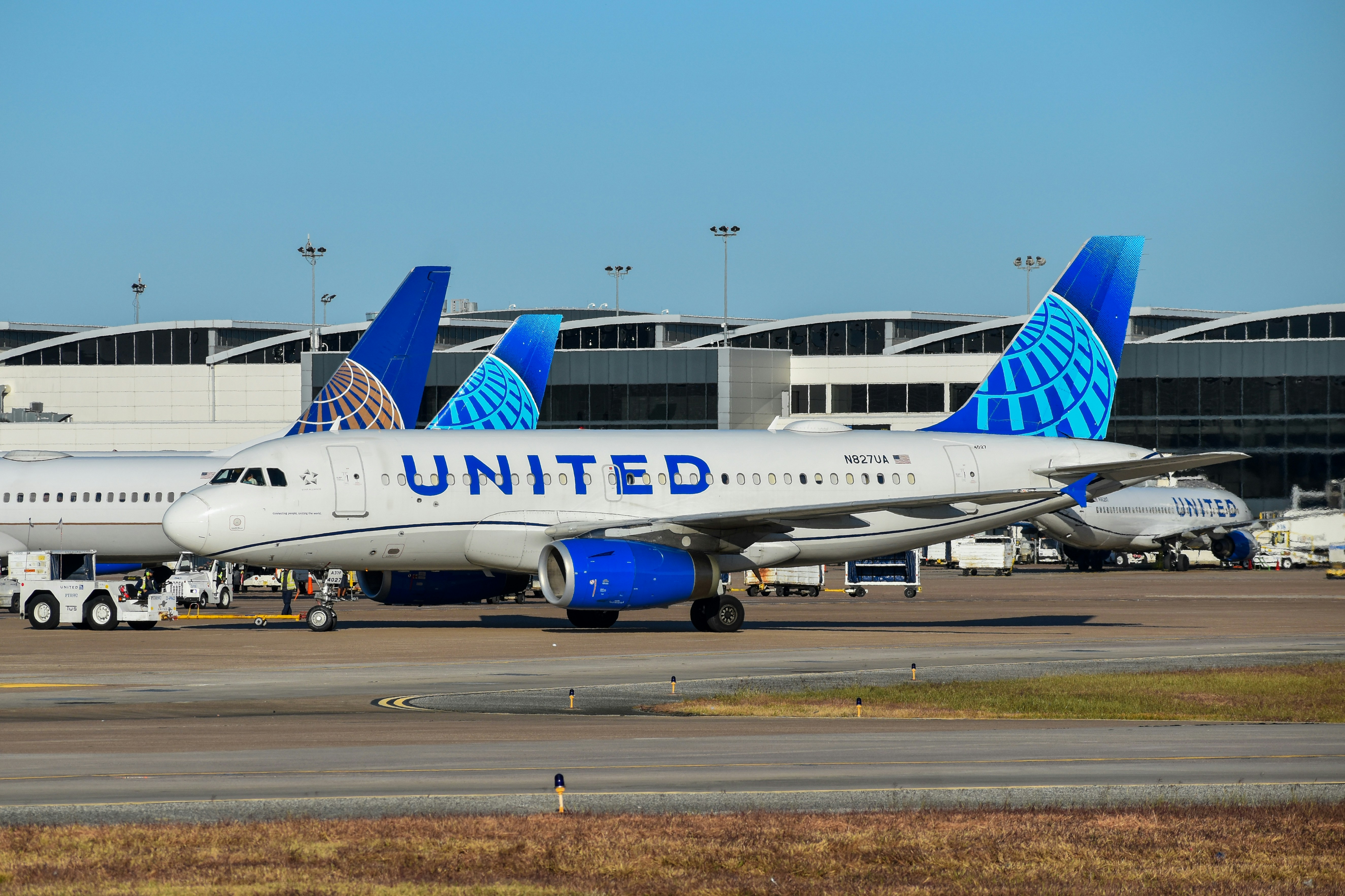 United Airlines planes aligned on the tarmac with a terminal in the background.