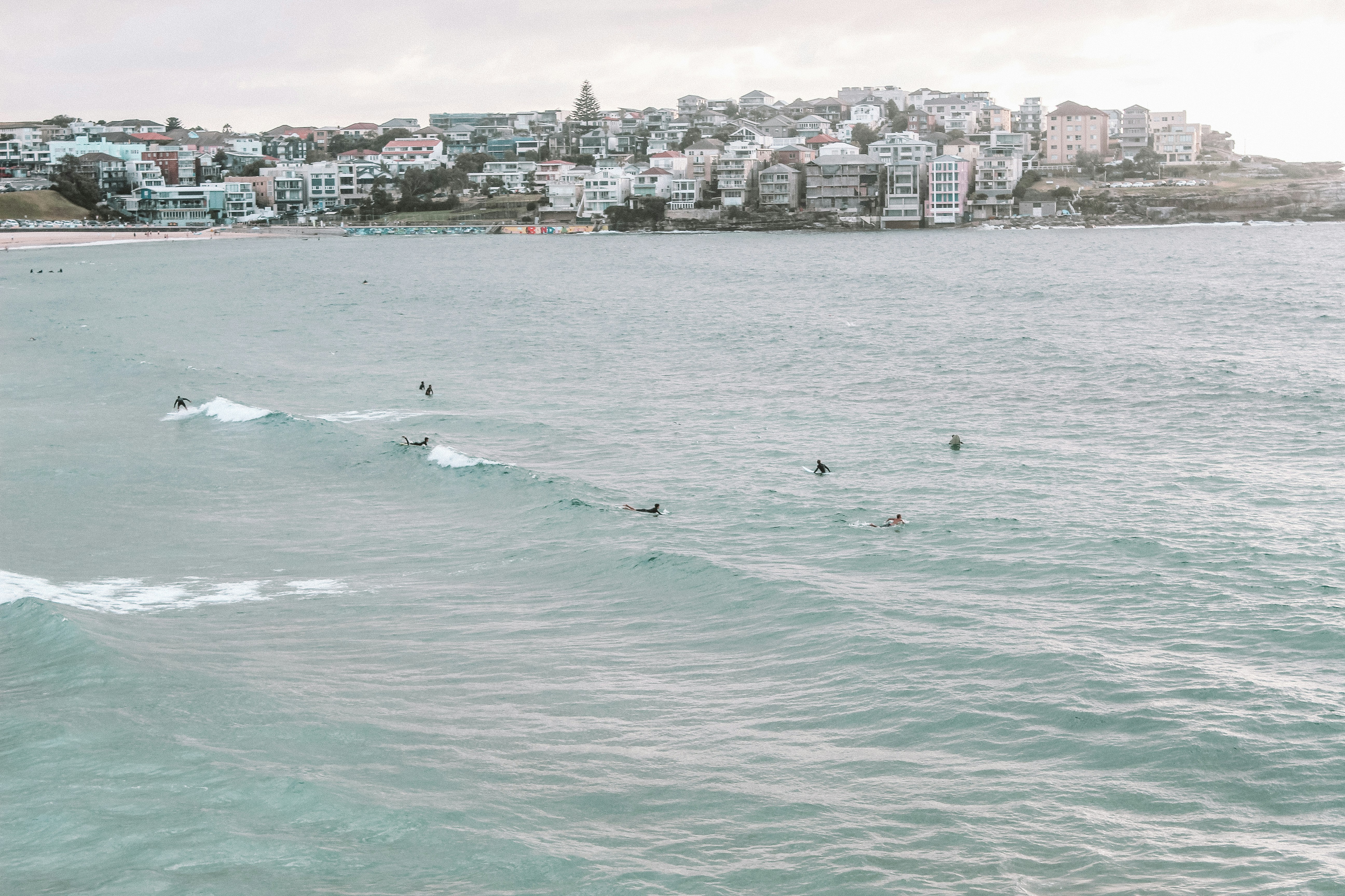 Quiet Morning Surf: Surfers Trace Subtle Waves Along a Distant Seaside Town