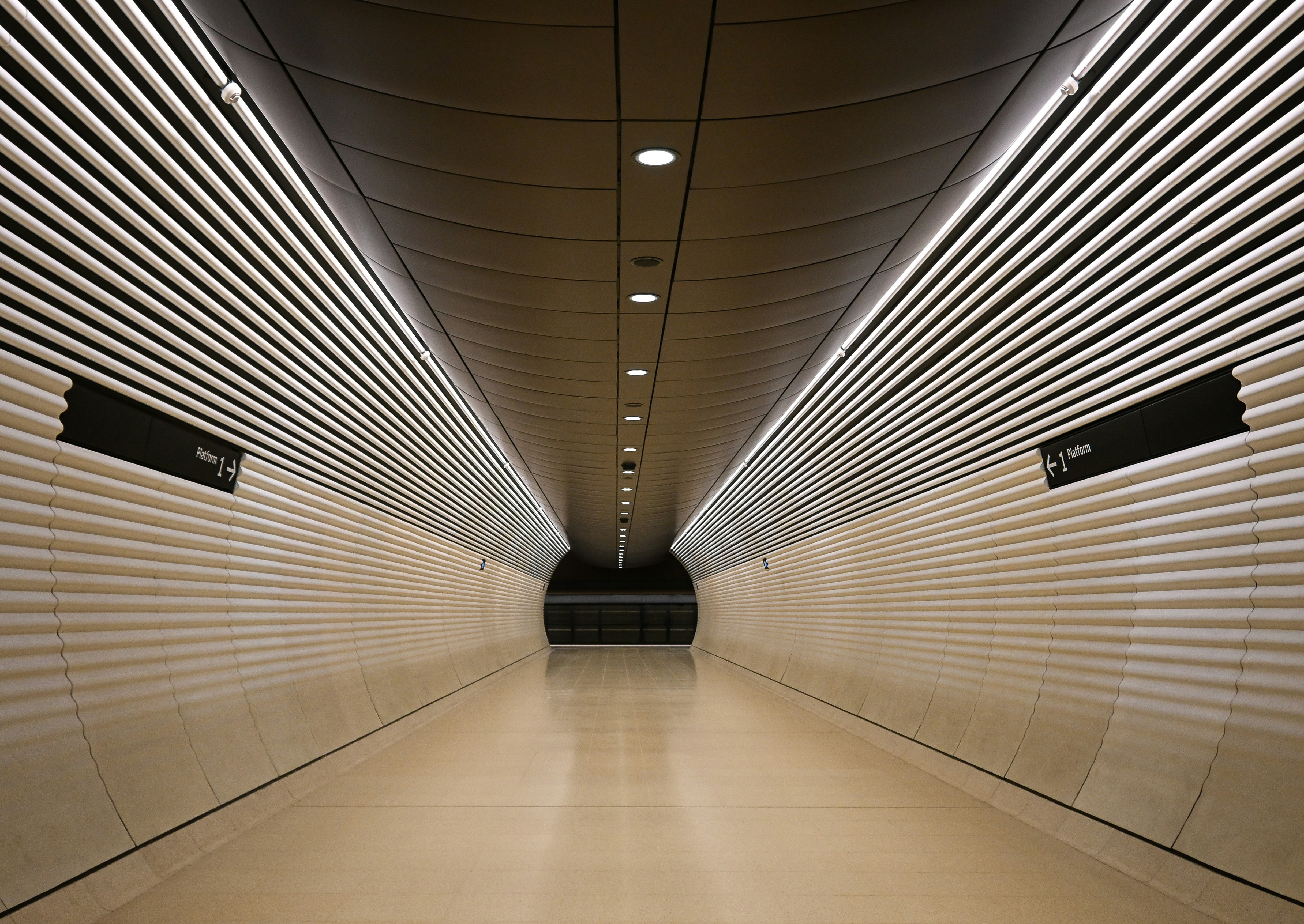 Deserted subway passageway with symmetrical modern design and metallic panels reflecting ambient lighting.