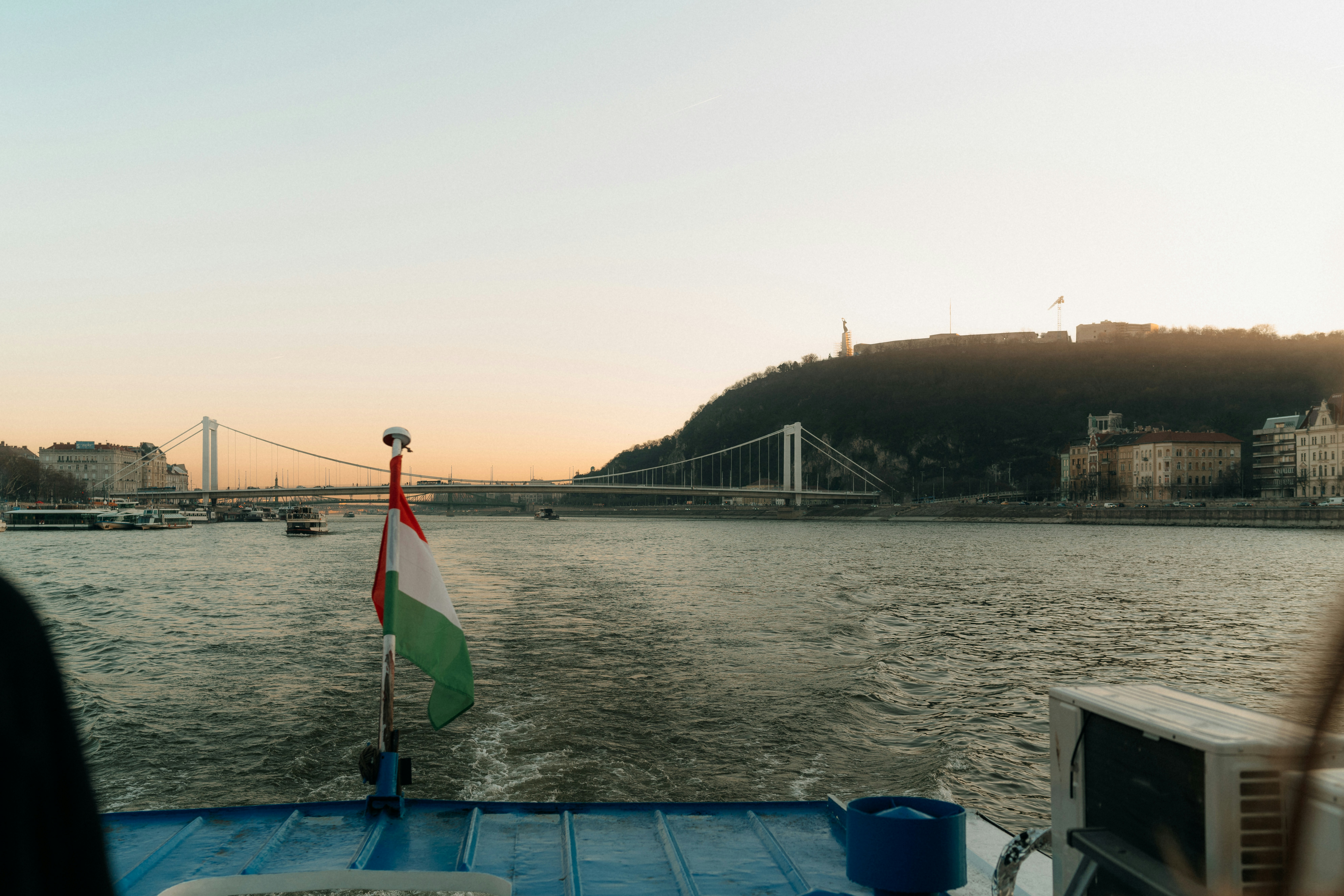 Harbor View from a Boat: Flag, Bridge, and Hills at Sunset