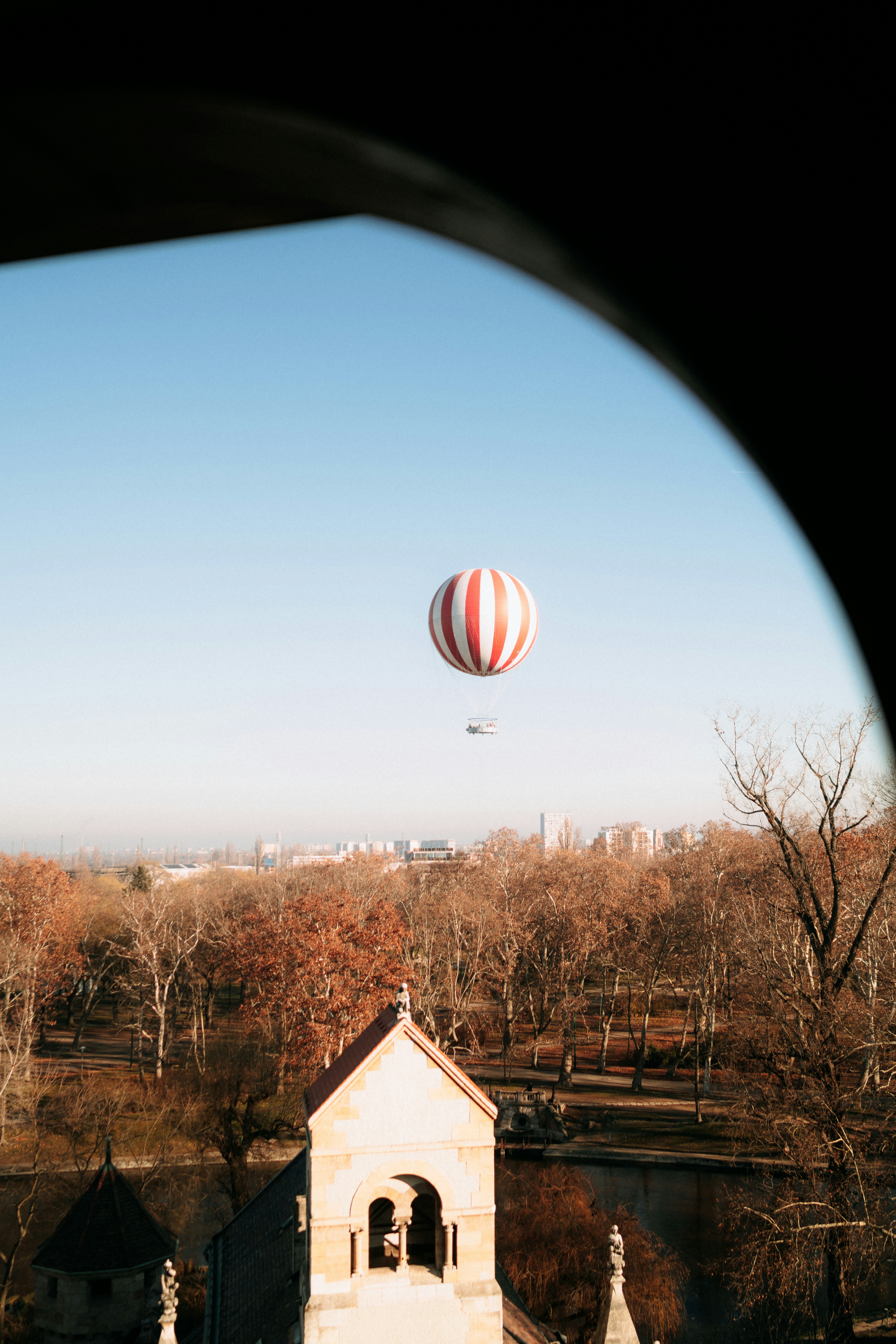 Crimson-Stripe Balloon Drifts Over a Stone Bell Tower in an Autumn Park