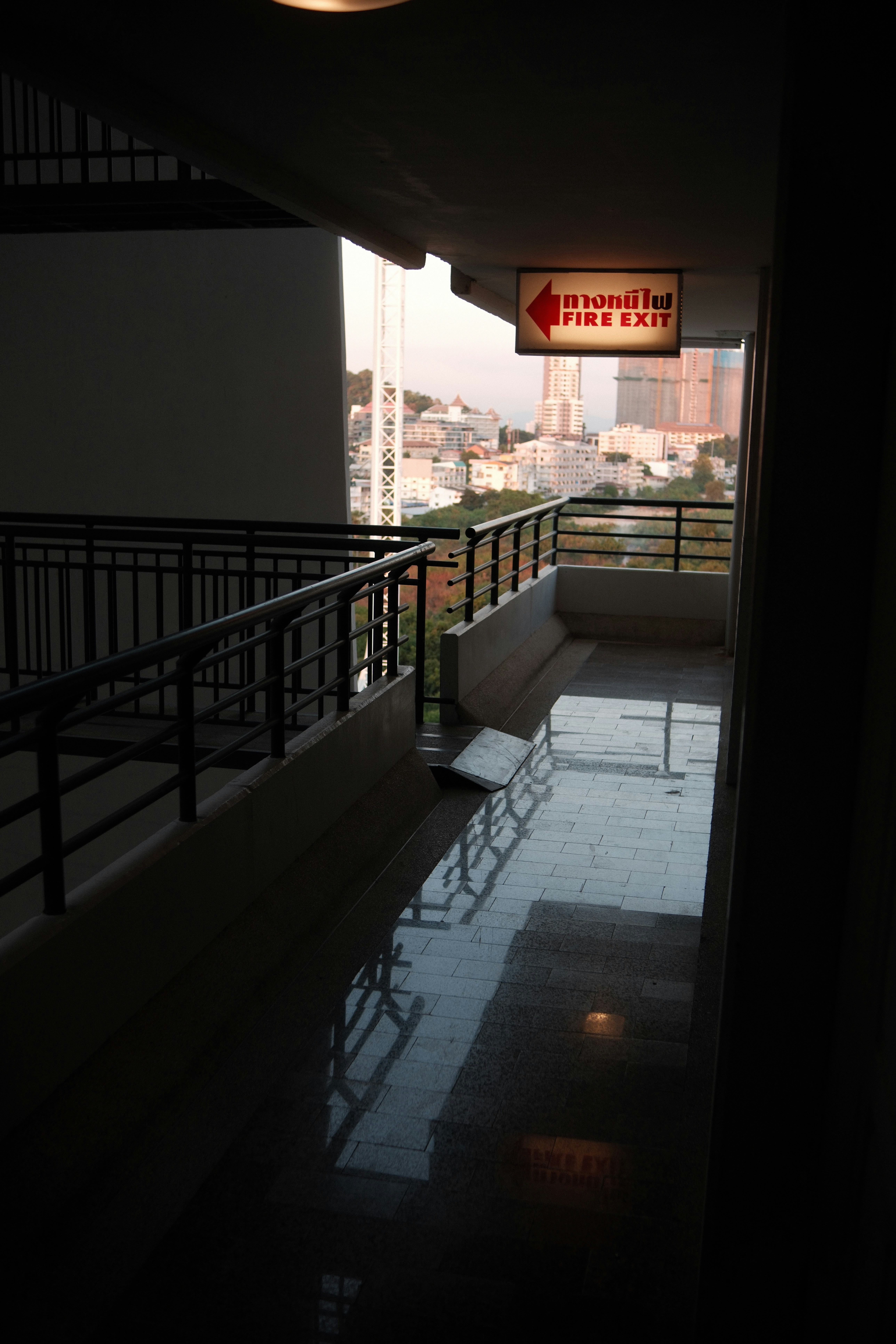 Fire Exit Beacon Framing a Quiet Corridor Toward the City at Dawn