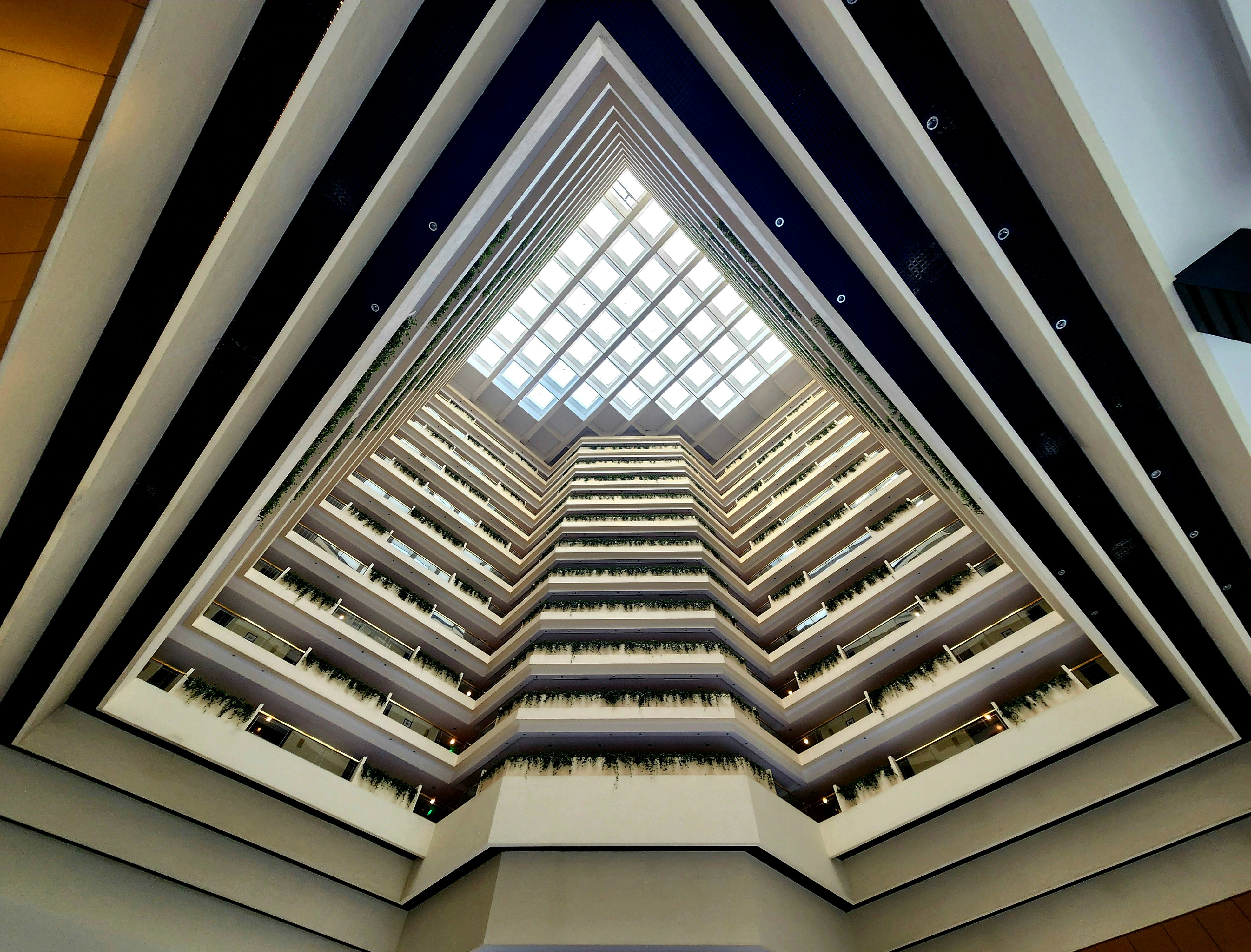 Atrium of a luxury hotel with geometric symmetry and lush balconies under a skylight.