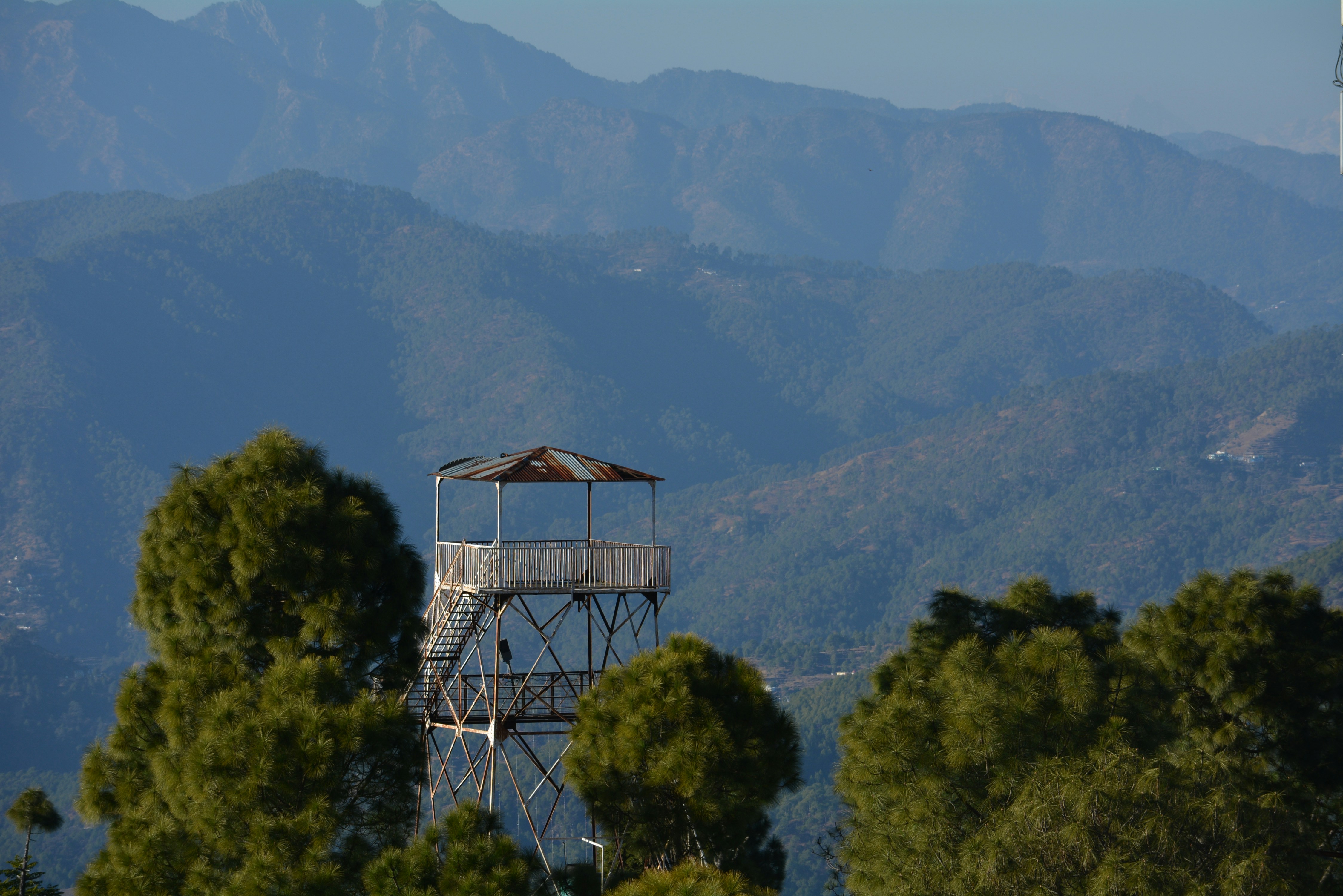A tower in the middle of a forest with mountains in the background ...