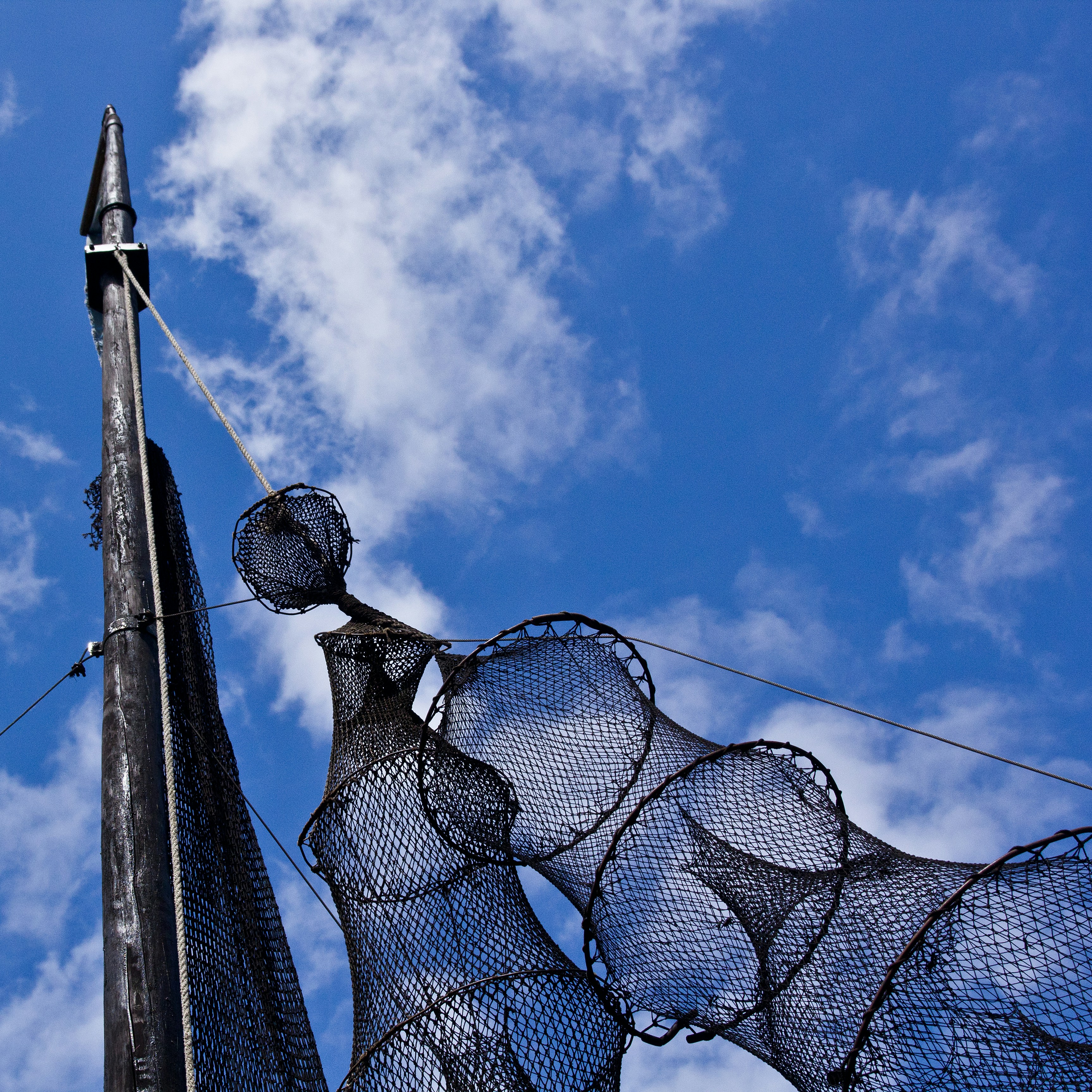 Black fishing net draped gracefully from a tall pole, set against a vibrant blue sky with scattered clouds.