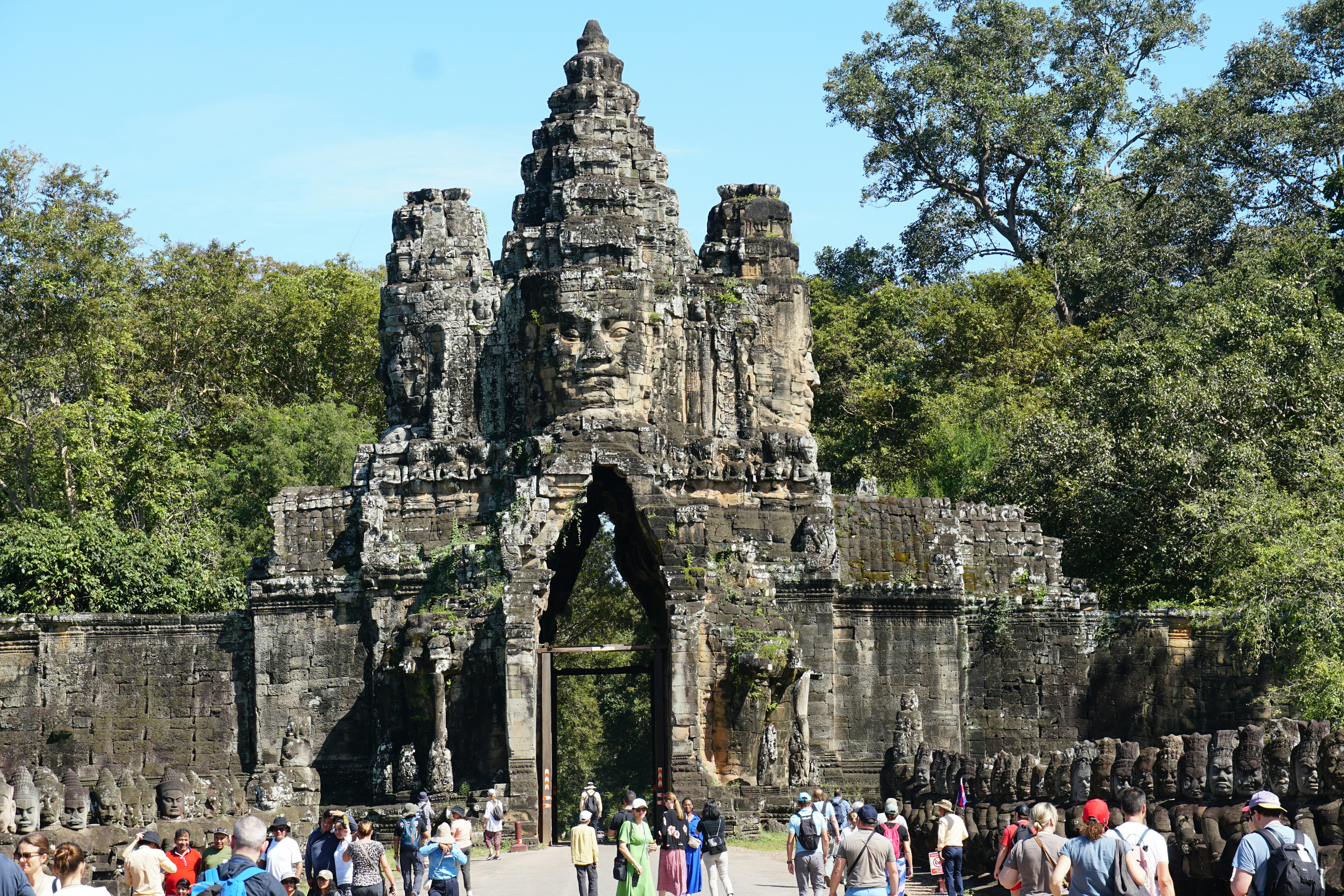 Crowd gathered around a historic stone gate adorned with intricate carvings under a clear sky.