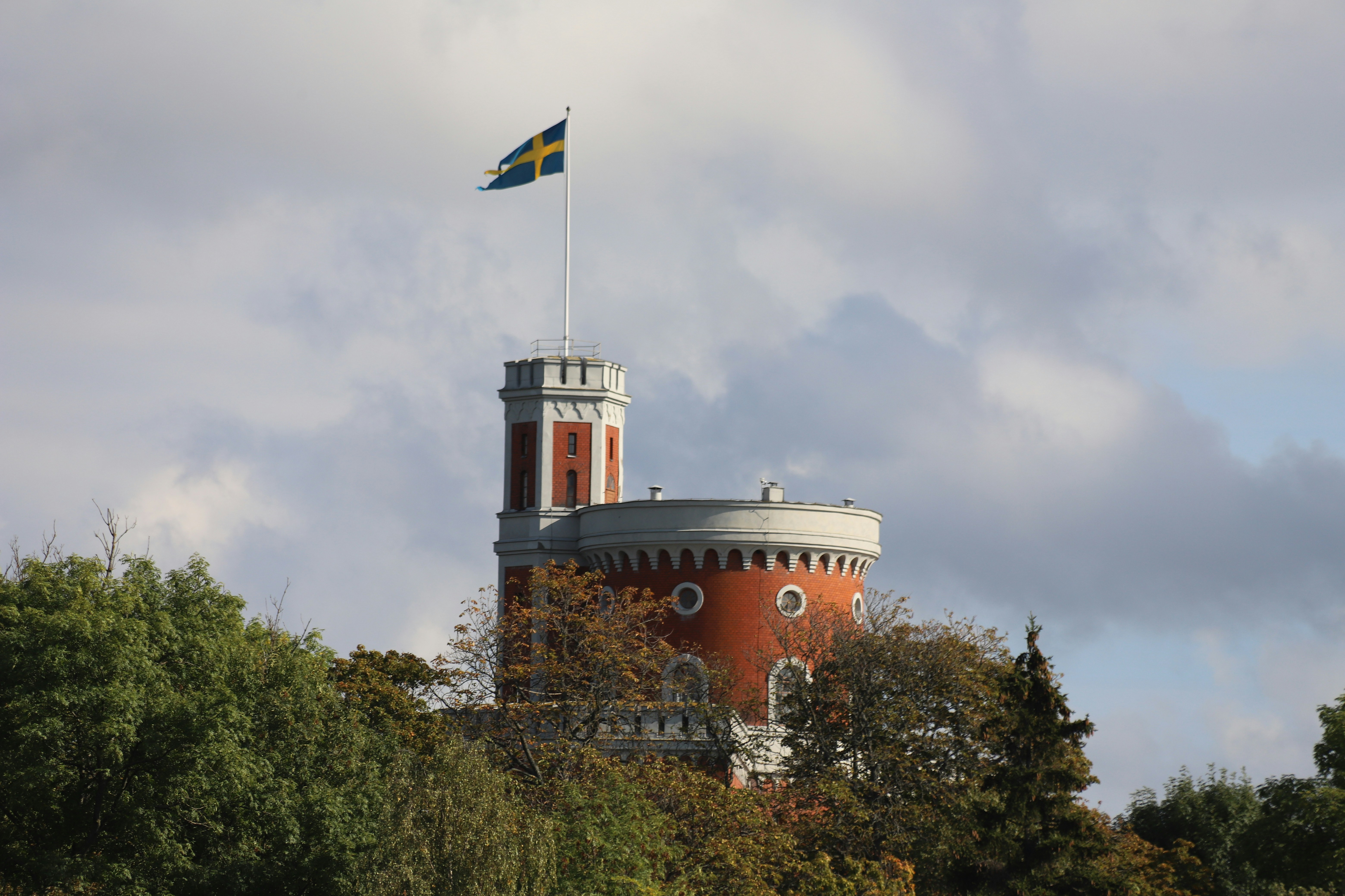 Swedish Flag Crowned Brick Turret Rising Above Autumn Canopy