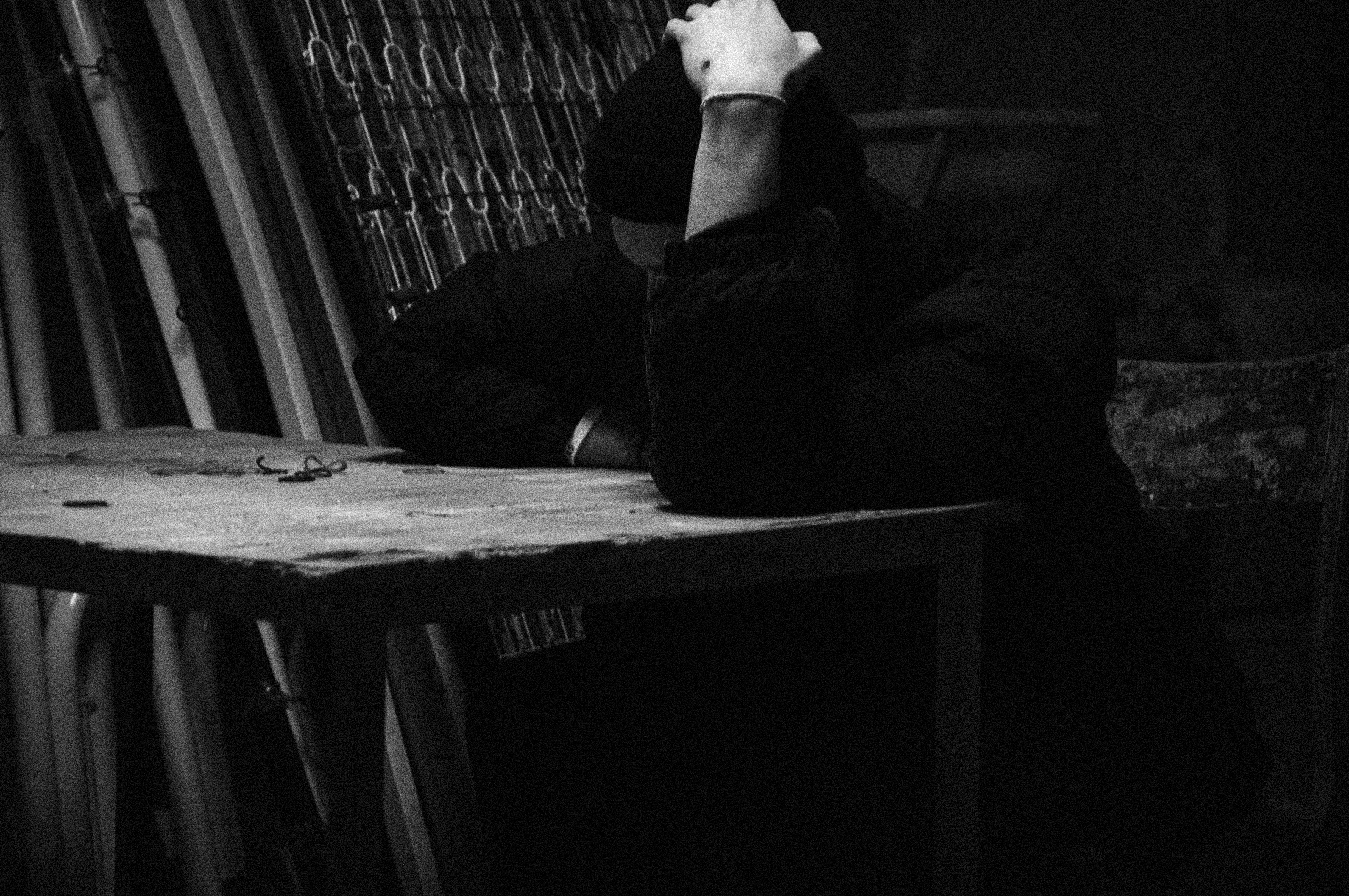 A person with their head down, resting on a table amidst a dimly lit environment, evoking a sense of introspection and solitude.