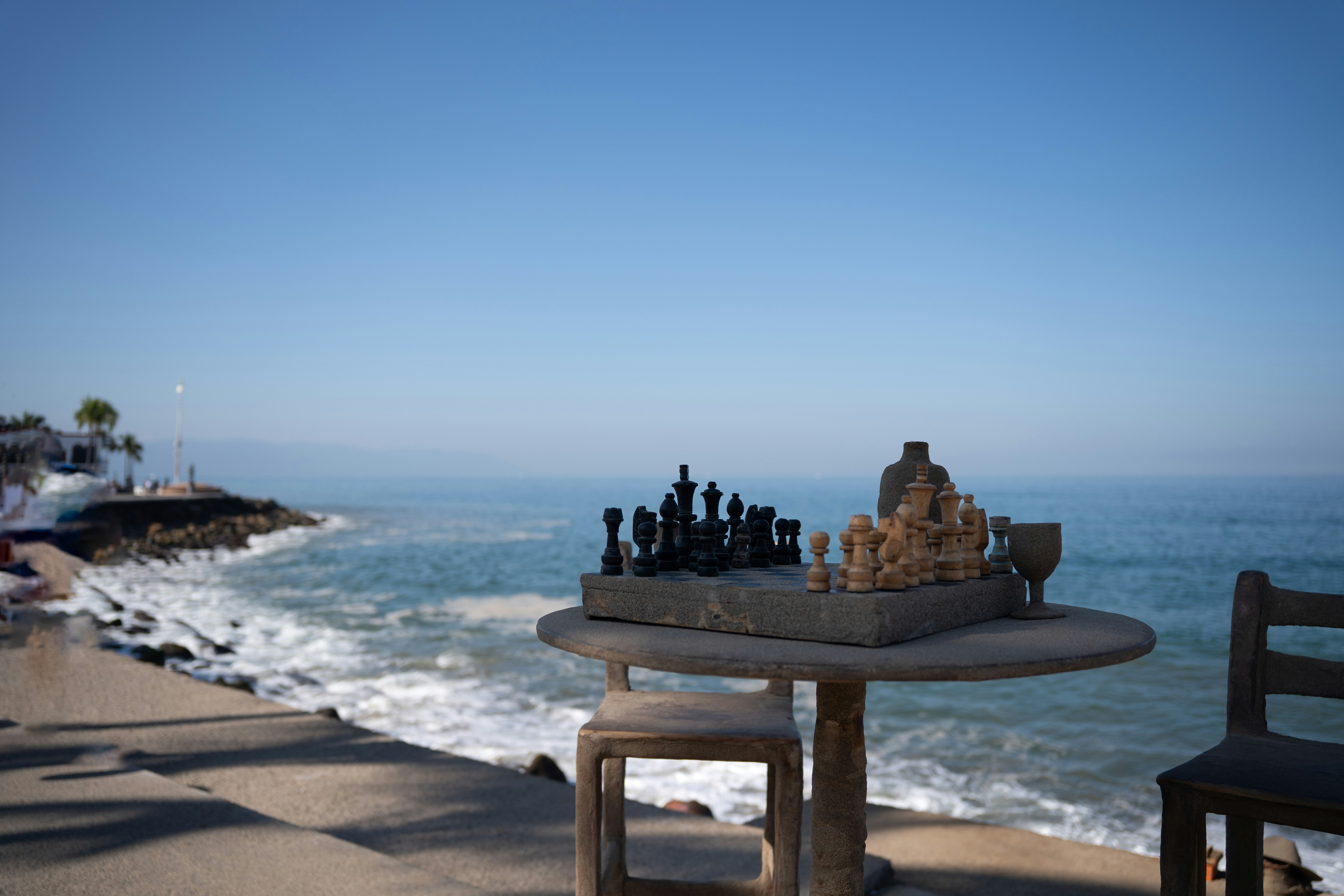 A table with a chess set on top of it next to the ocean photo – Free ...