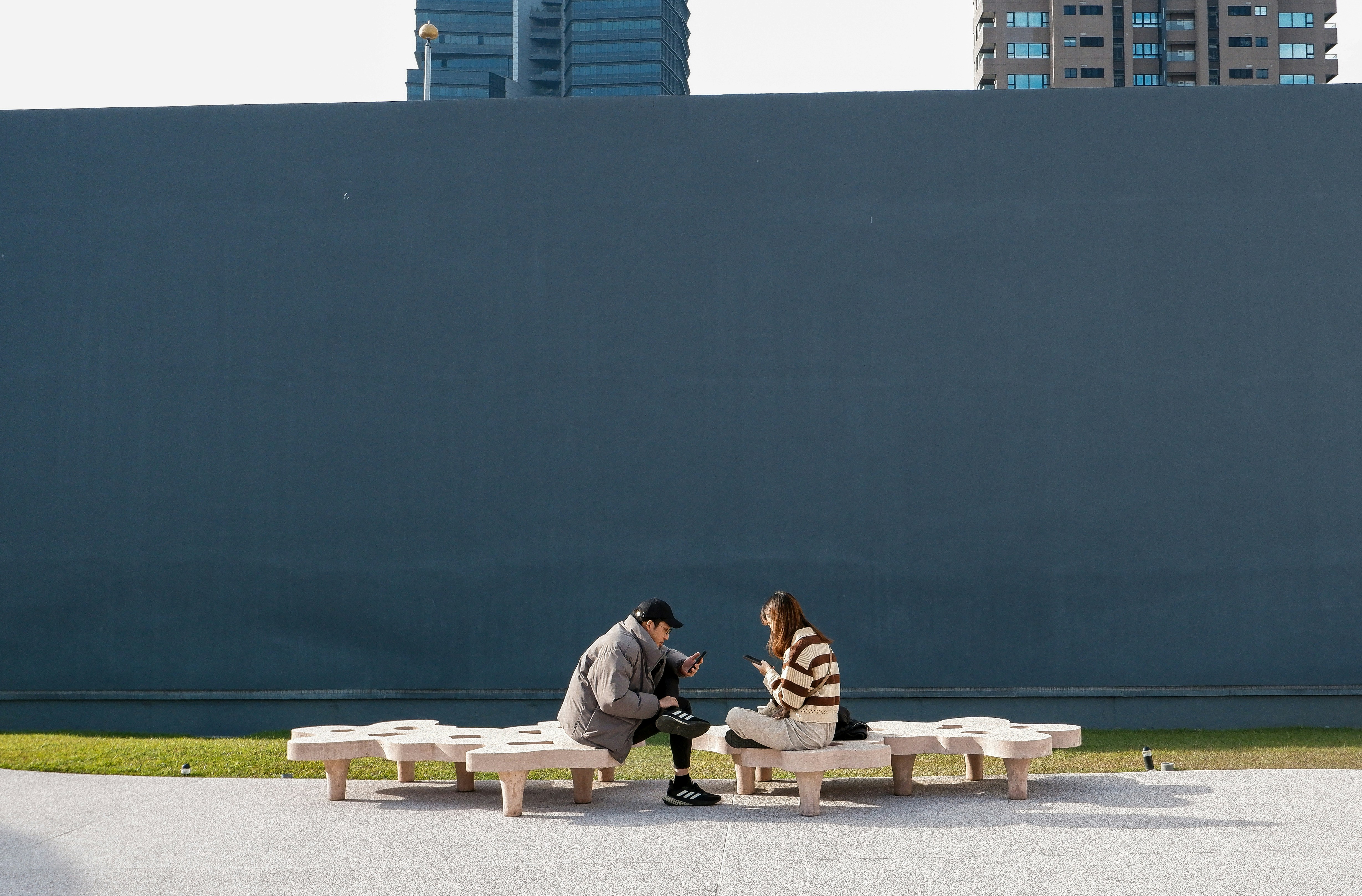 Quiet Exchange on White Benches Before a Monolithic Blue Wall