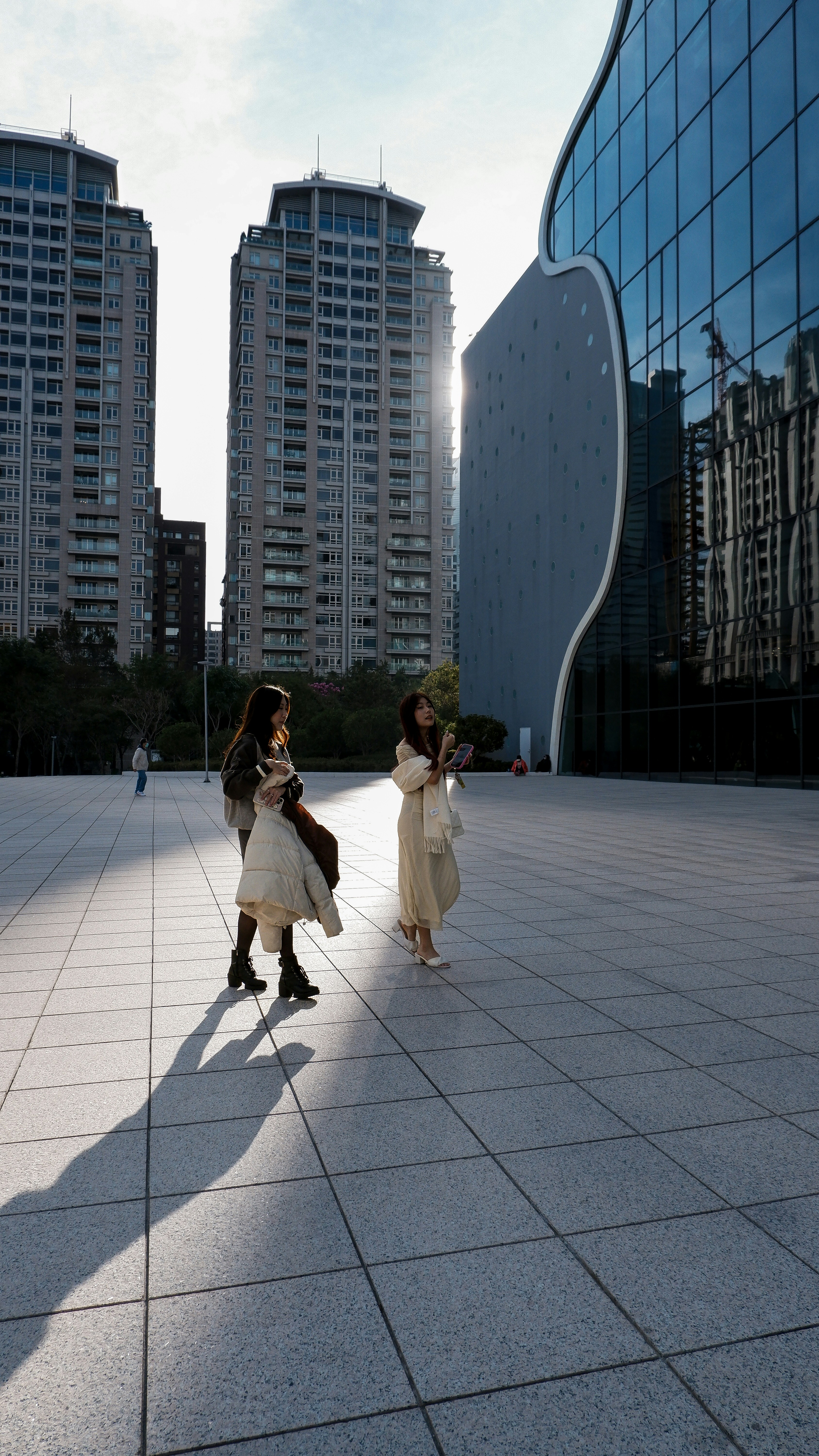 Two Women, Long Shadows, and a Glass-Curve Facade