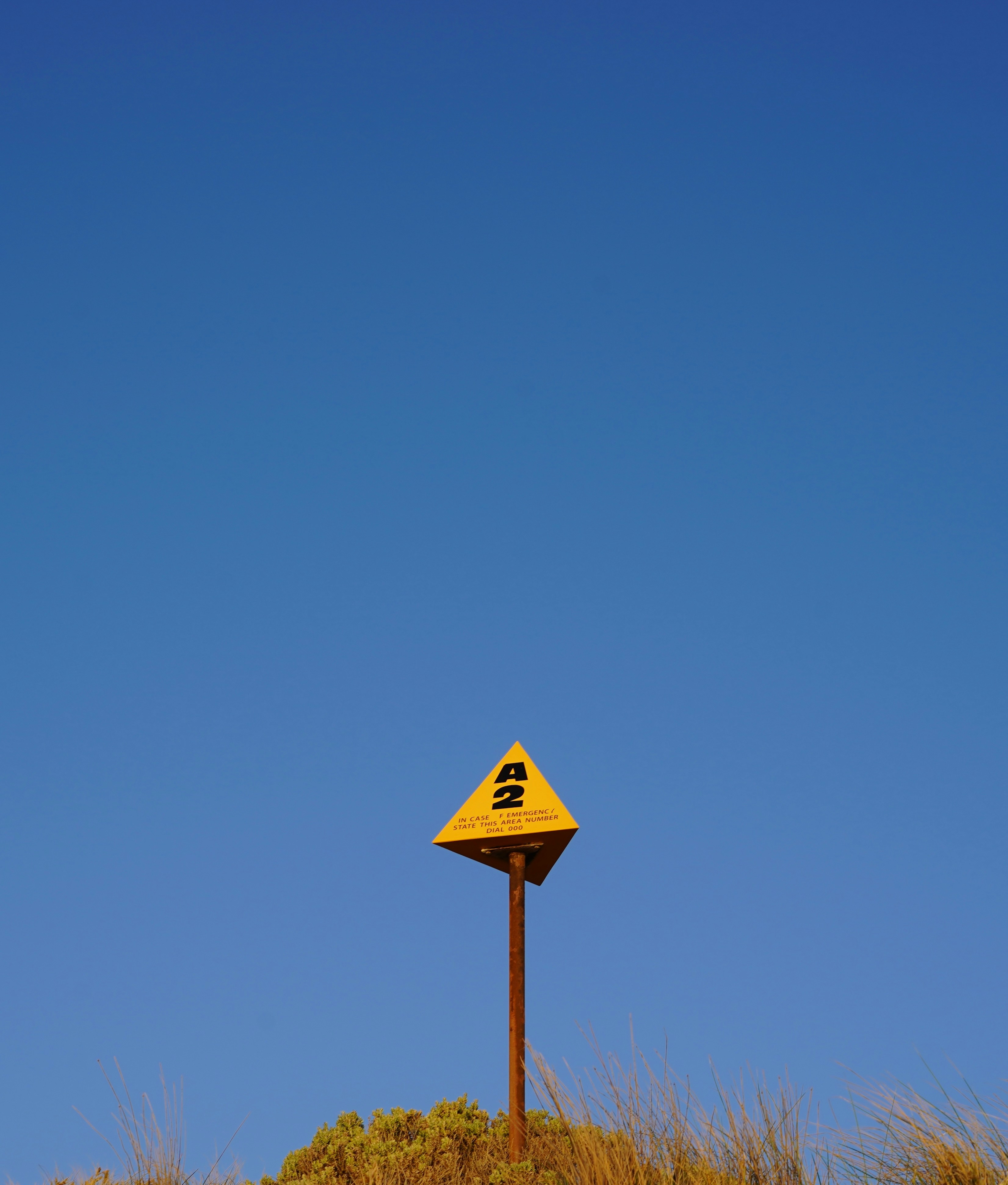 Yellow triangular warning sign marked '2' stands on a wooden post against a clear blue sky.