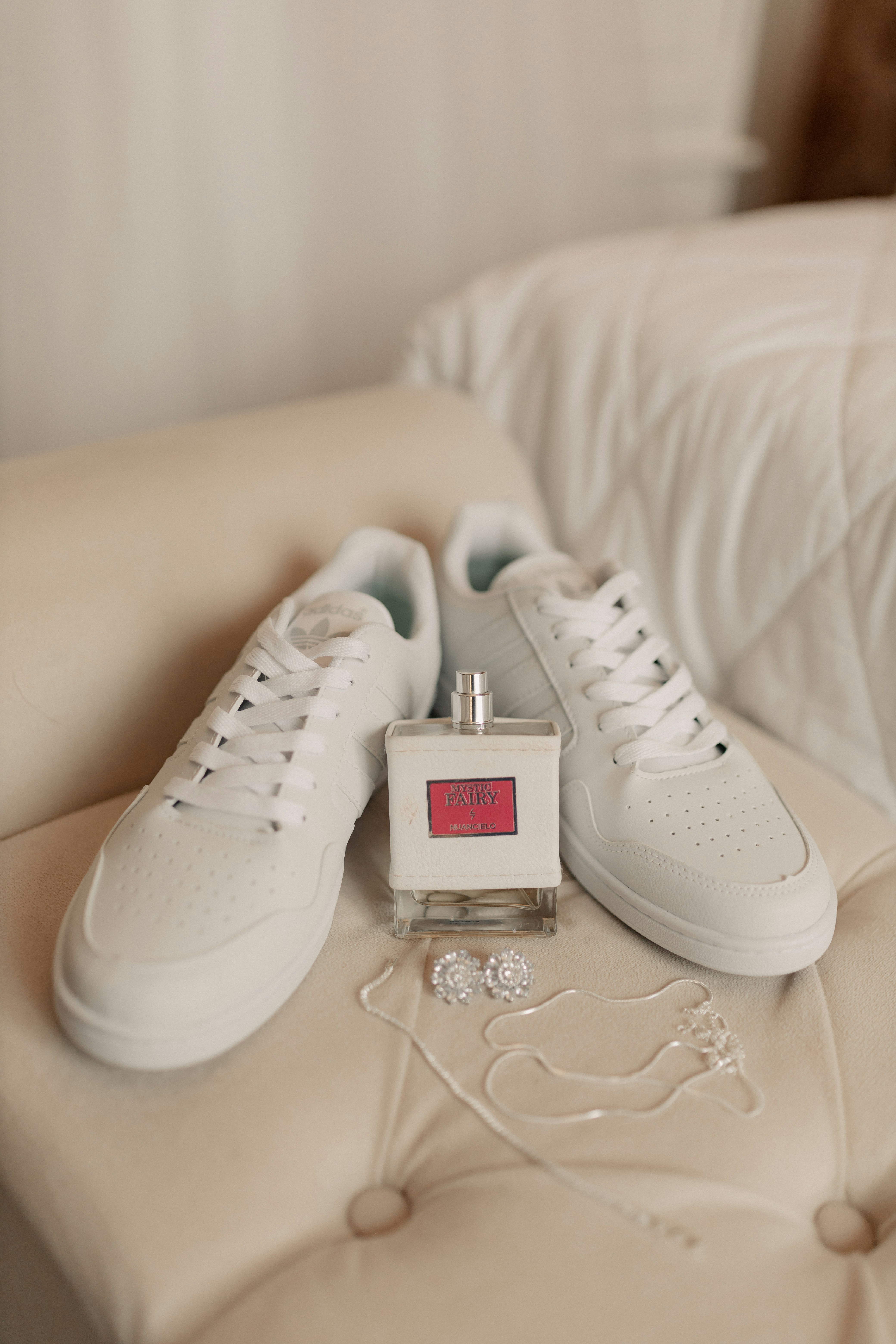 White sneakers cradle a perfume bottle and jewelry on a tufted surface