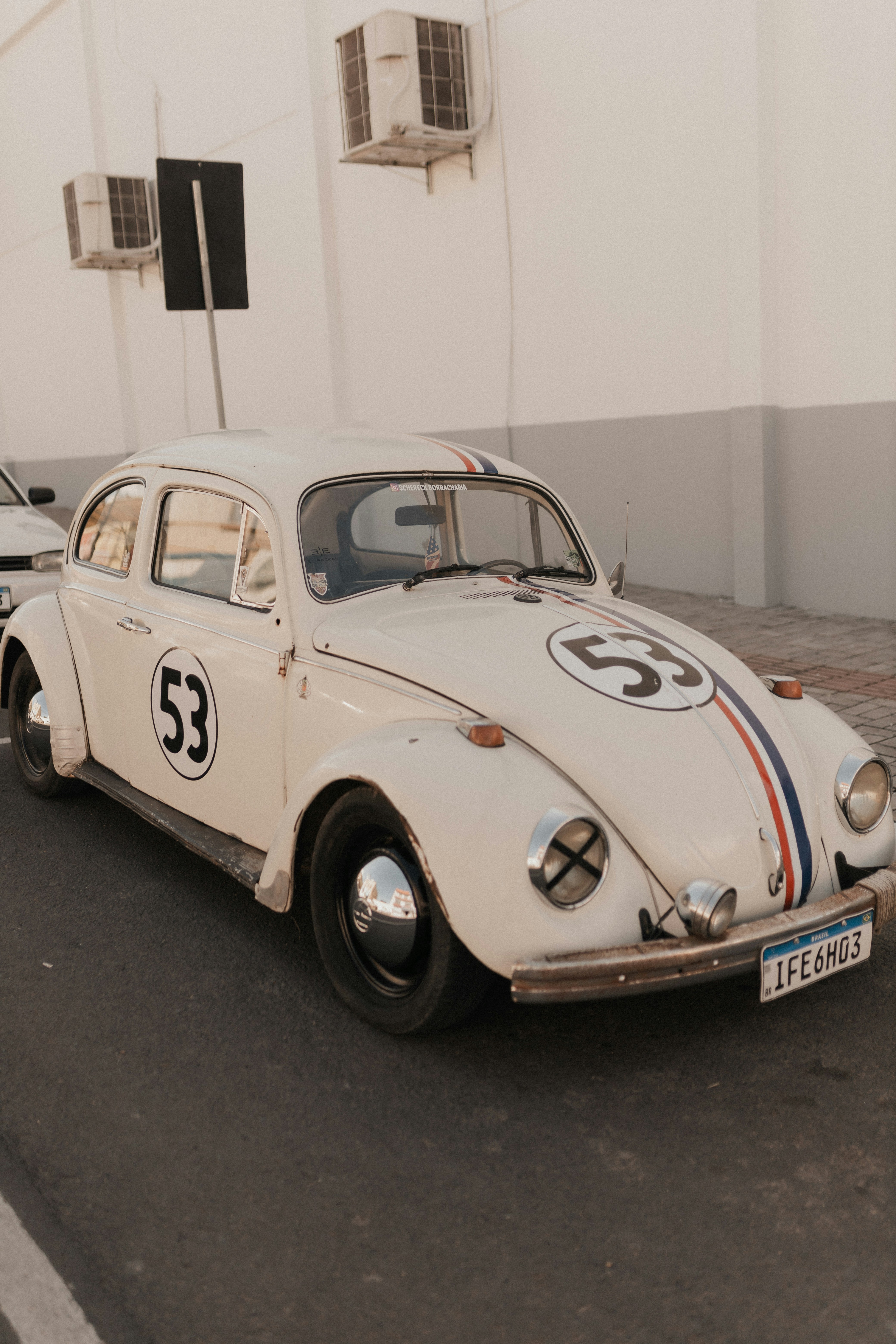 A white vw bug driving down a street next to a white building photo ...