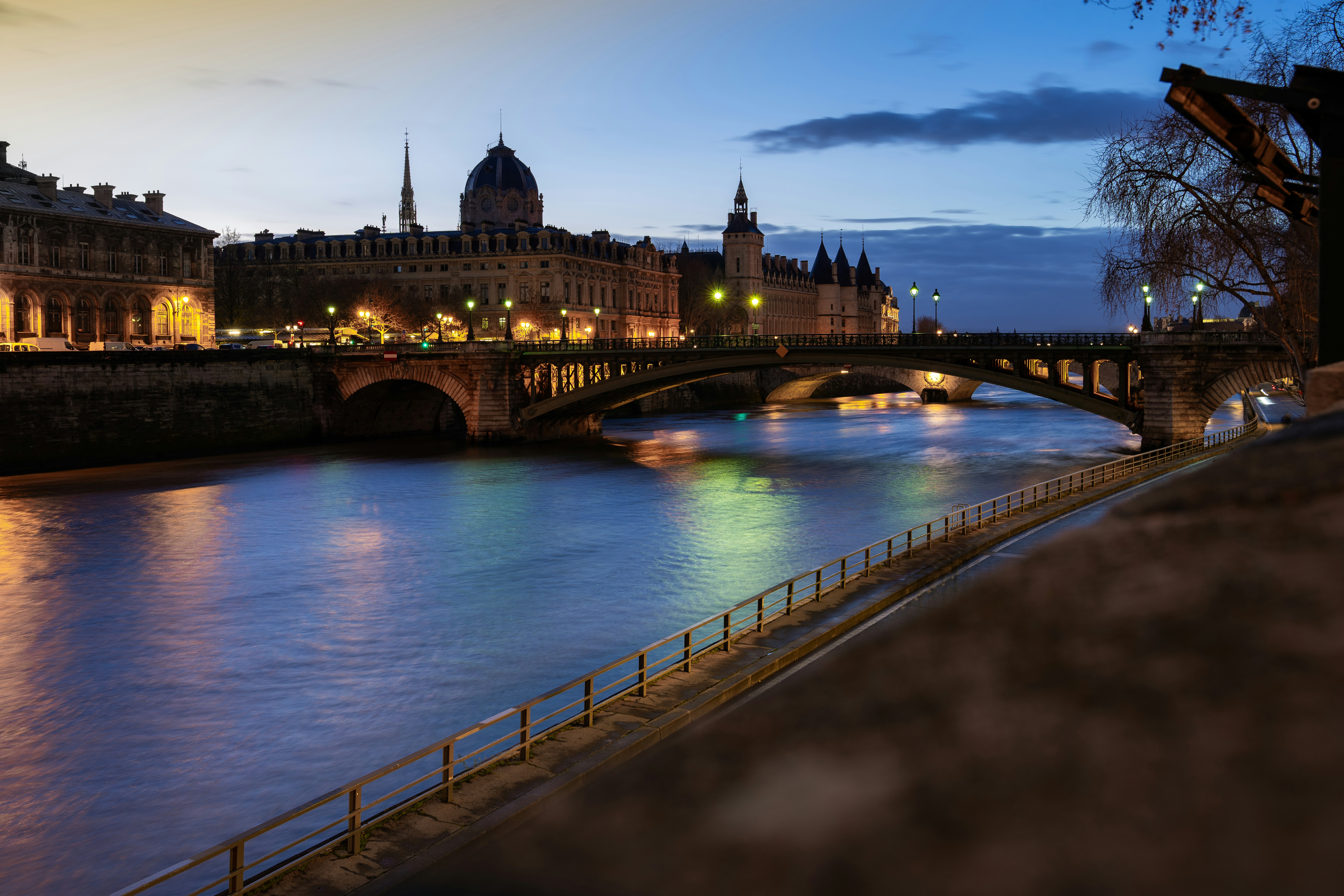 City river glistens under a twilight sky, flanked by historic architecture and a gracefully arched bridge.