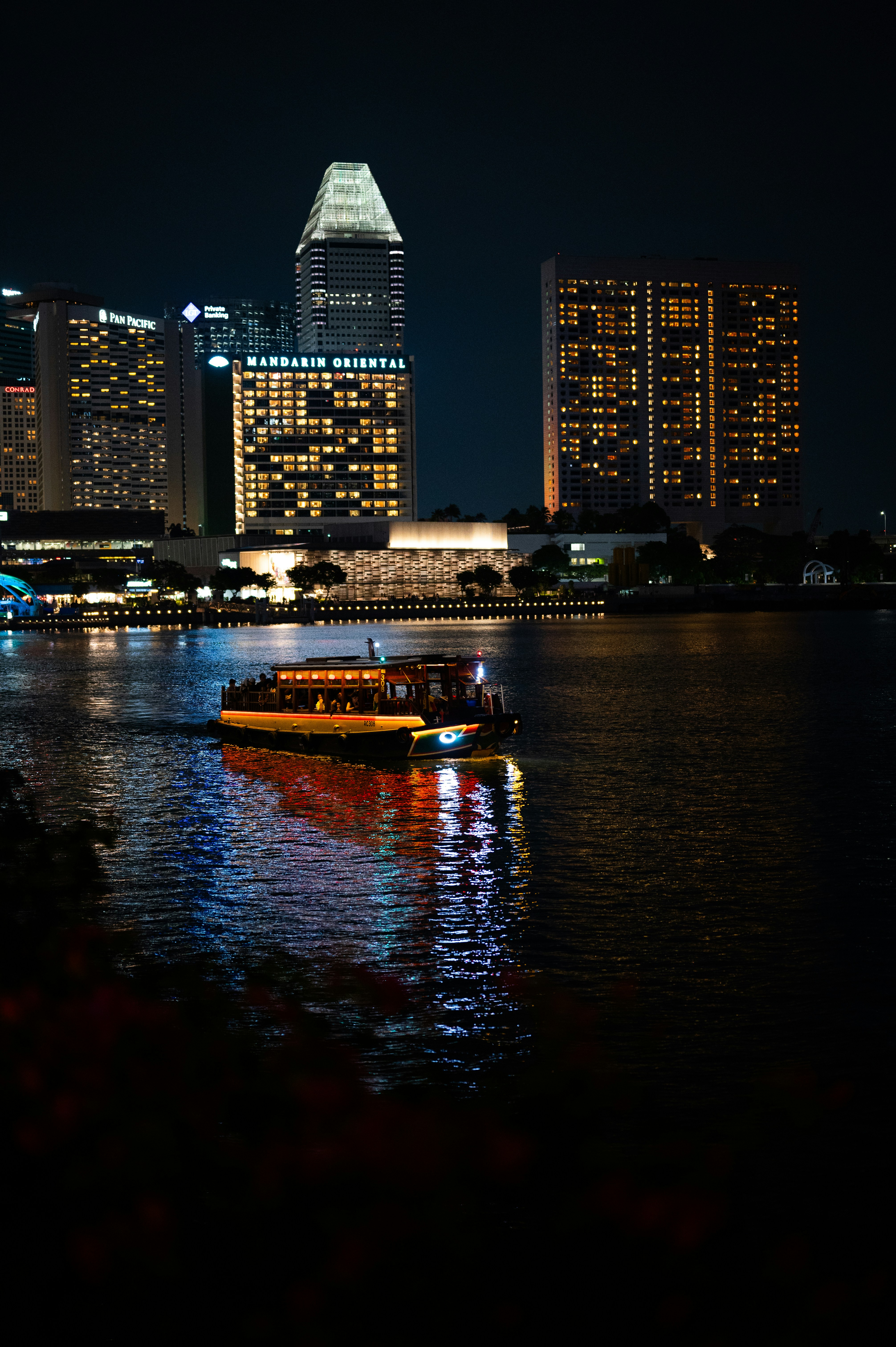 Boat cruising on a river with illuminated skyscrapers in the background at night.