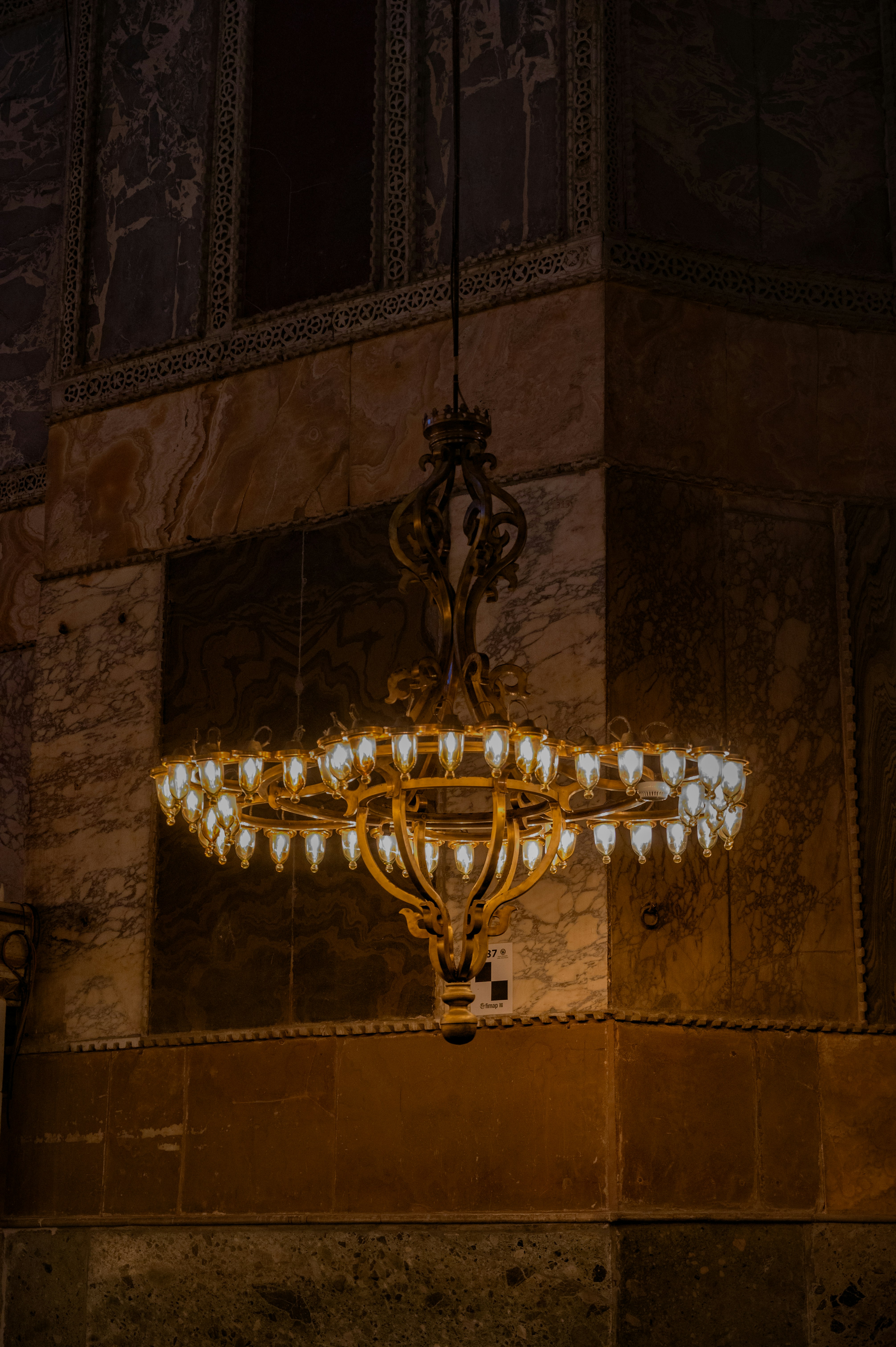Chandelier halo: a gilded circular beacon in a dim marble hall