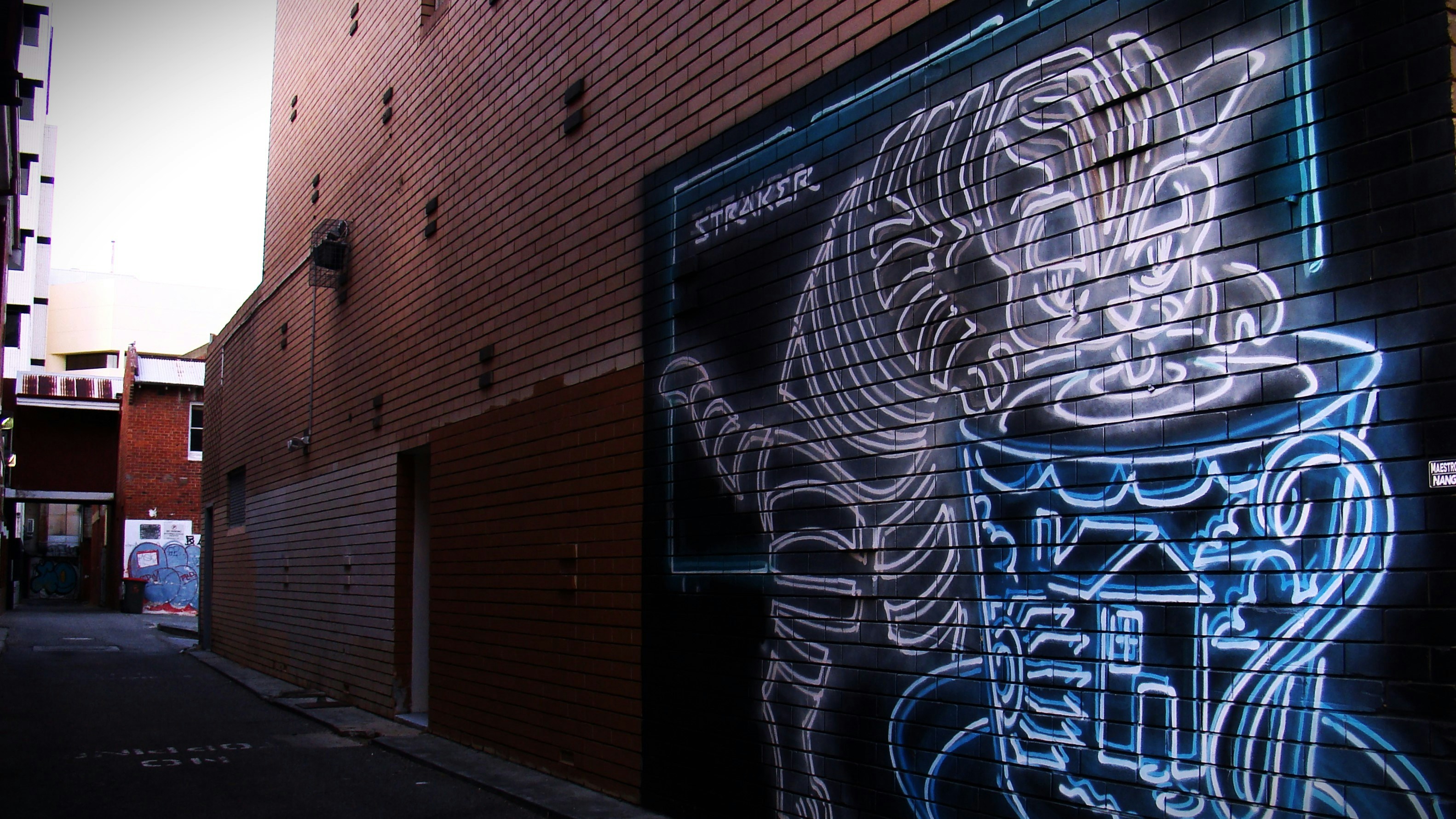 Vibrant street art featuring a whimsical tiger interacting with a cup, set against a brick alleyway backdrop.