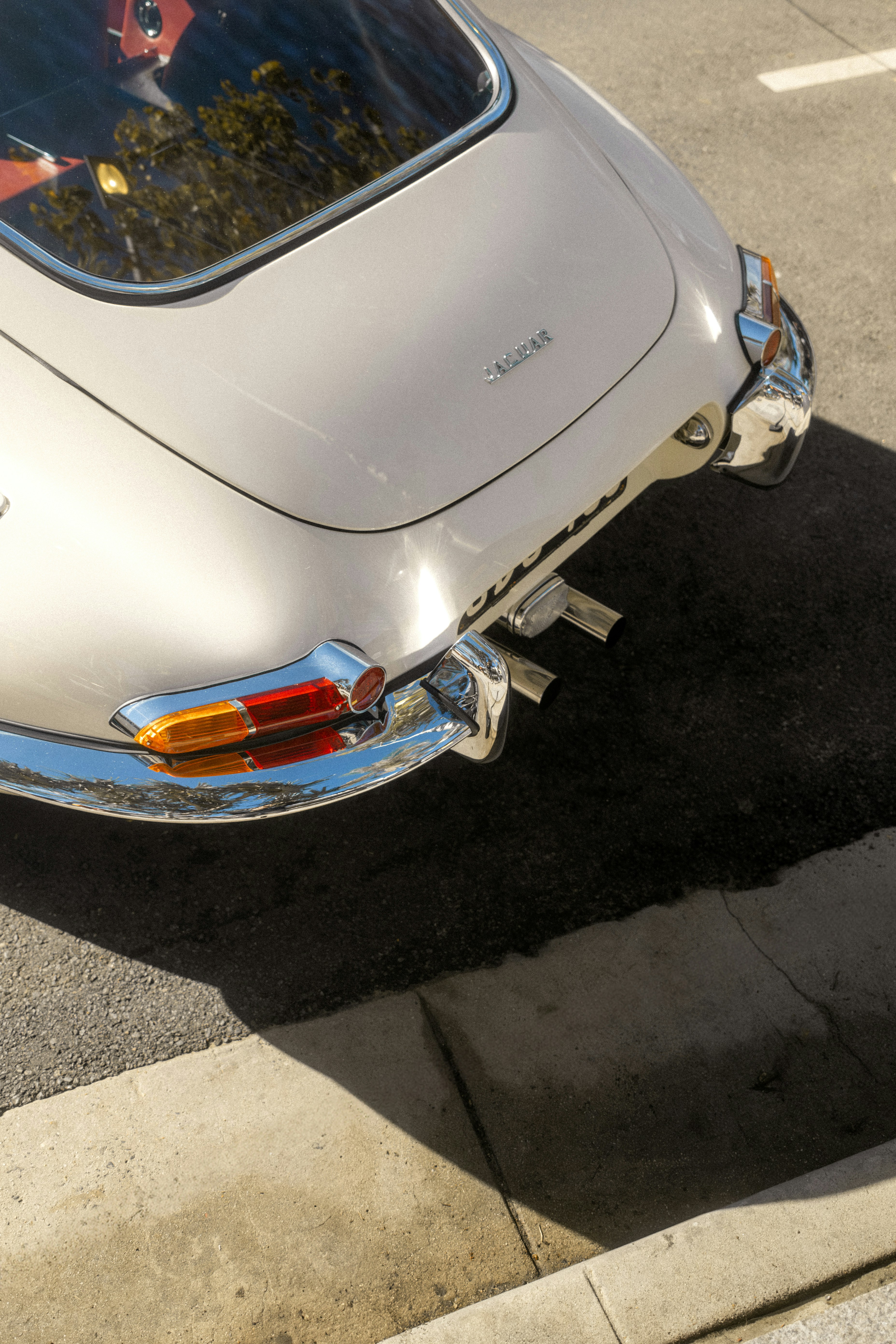 Rear view of a silver 1962 Jaguar E-Type highlighting its sleek curves and chrome details under warm sunlight.