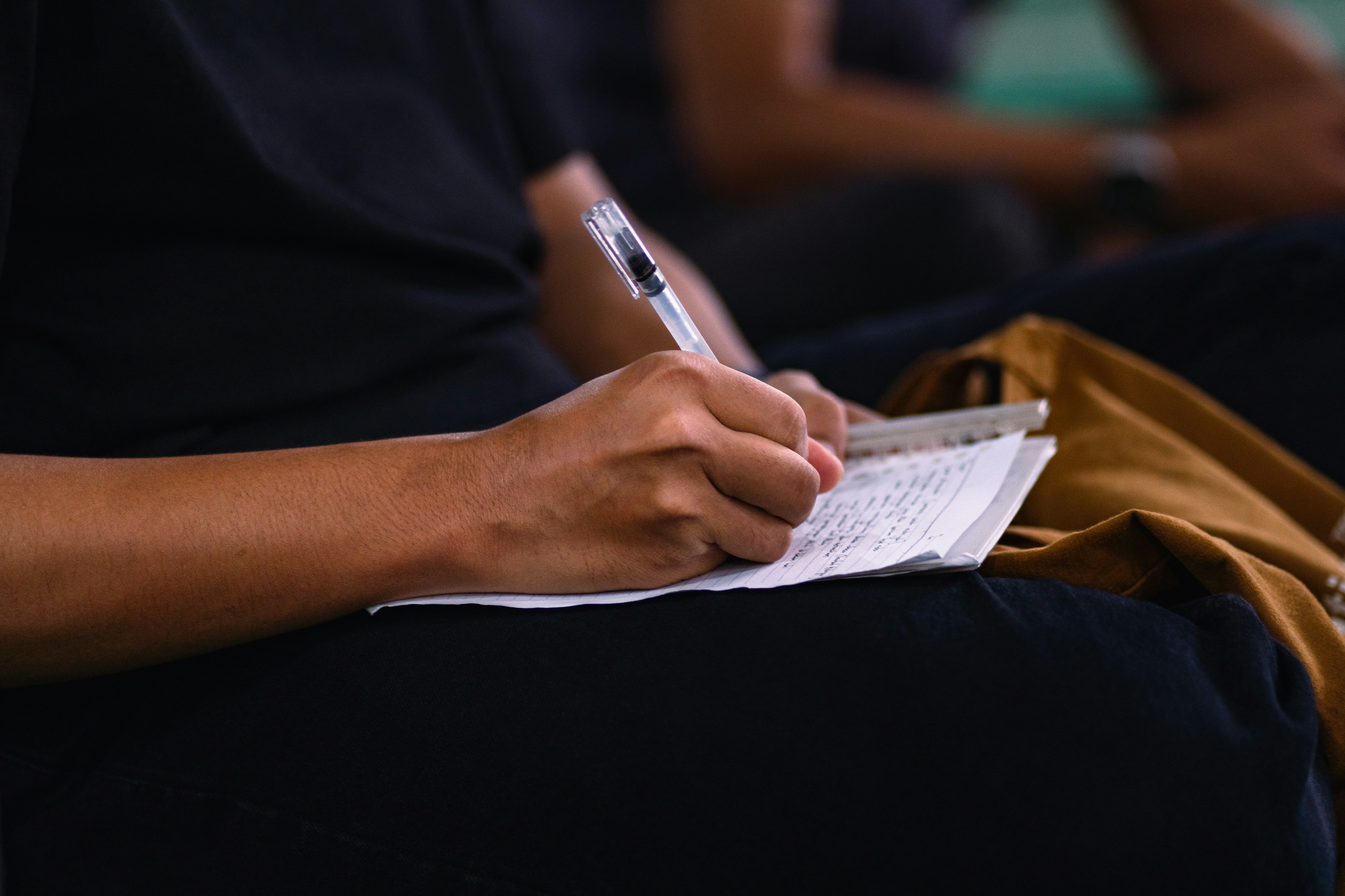 A person sitting down writing on a piece of paper photo – Free Pen ...